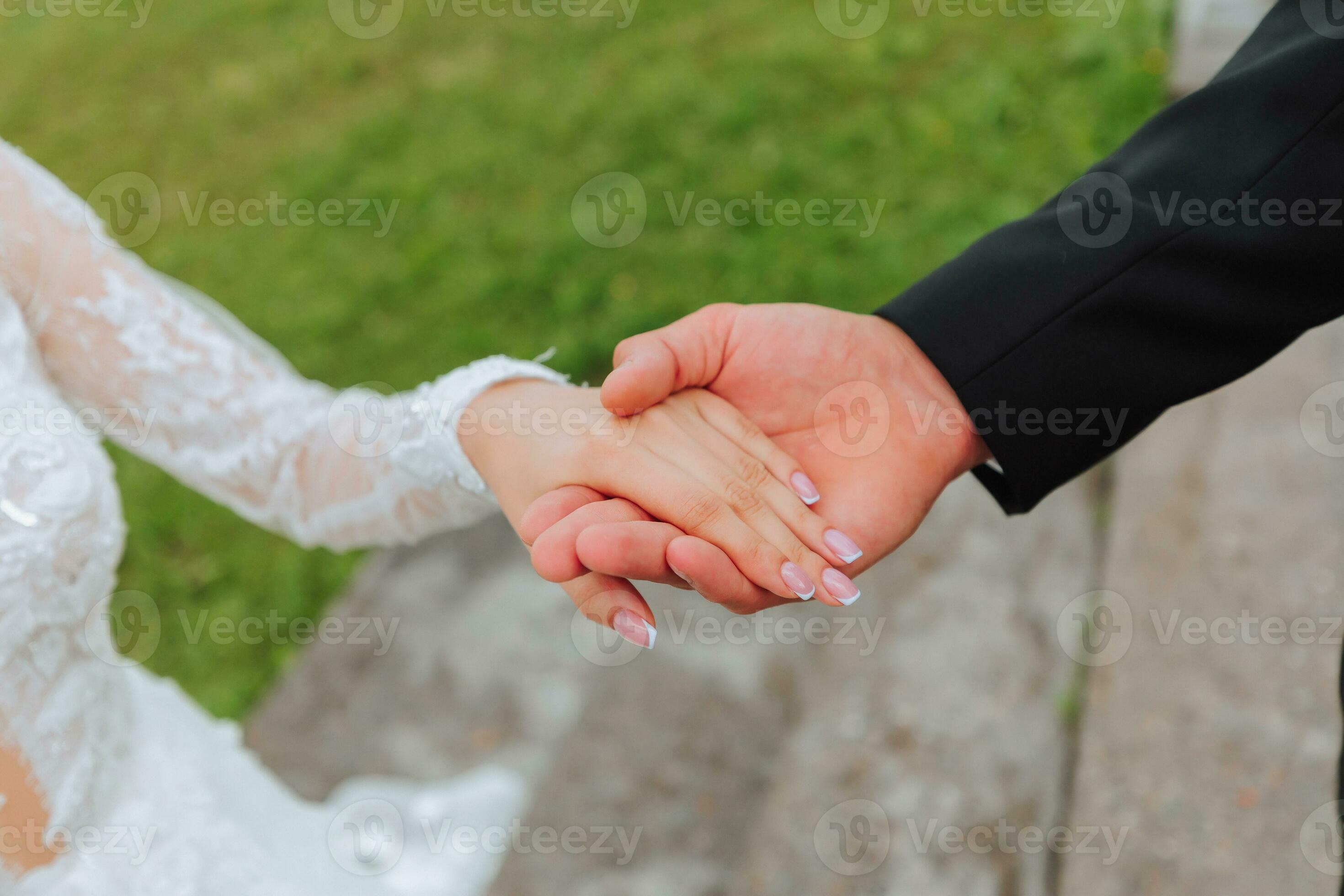 Hands of the bride and groom close-up. The groom holds the bride's hand ...
