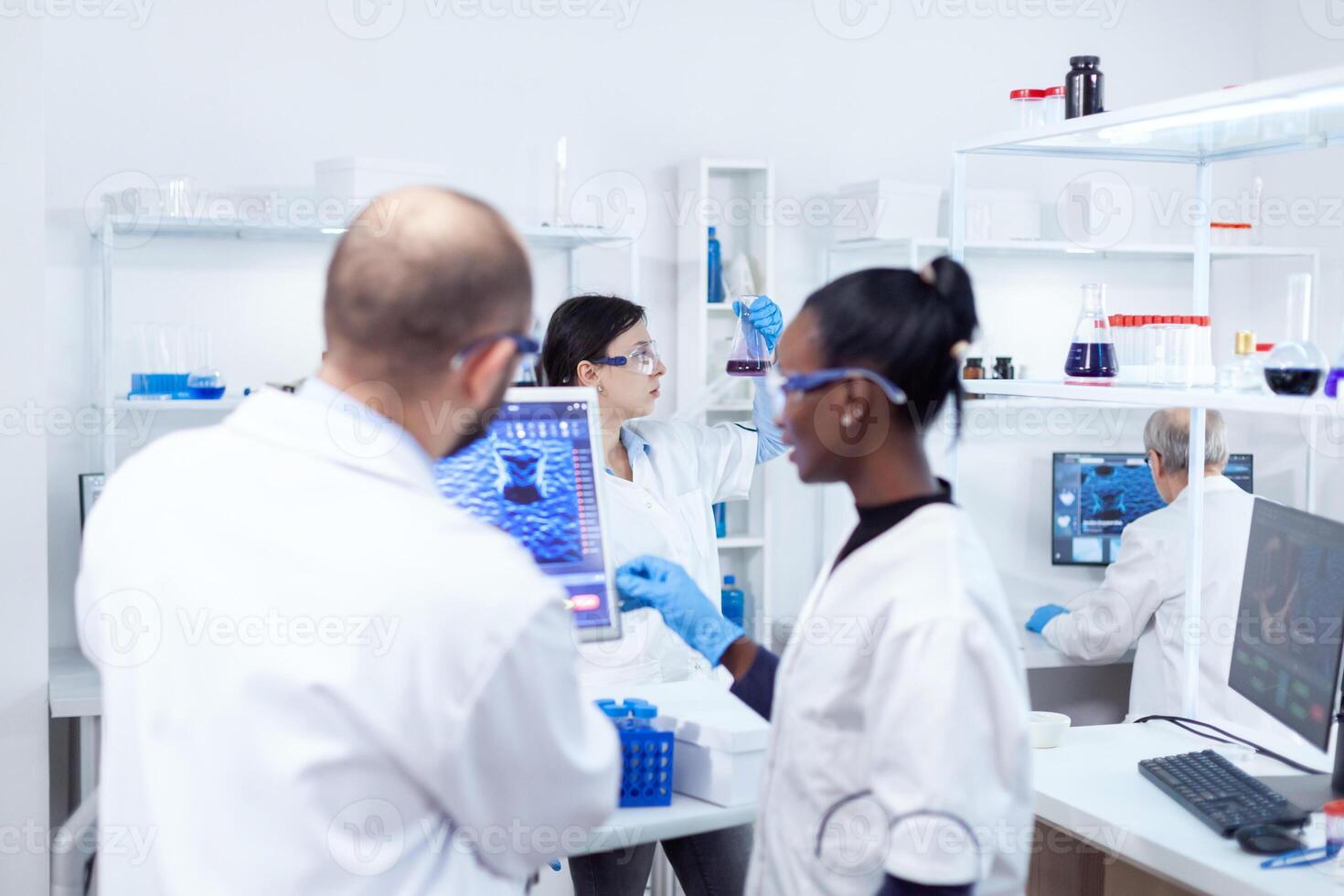 Scientist holding glass flask with blue genetic material in busy ... Scientist holding glass flask with blue genetic material in busy ...
