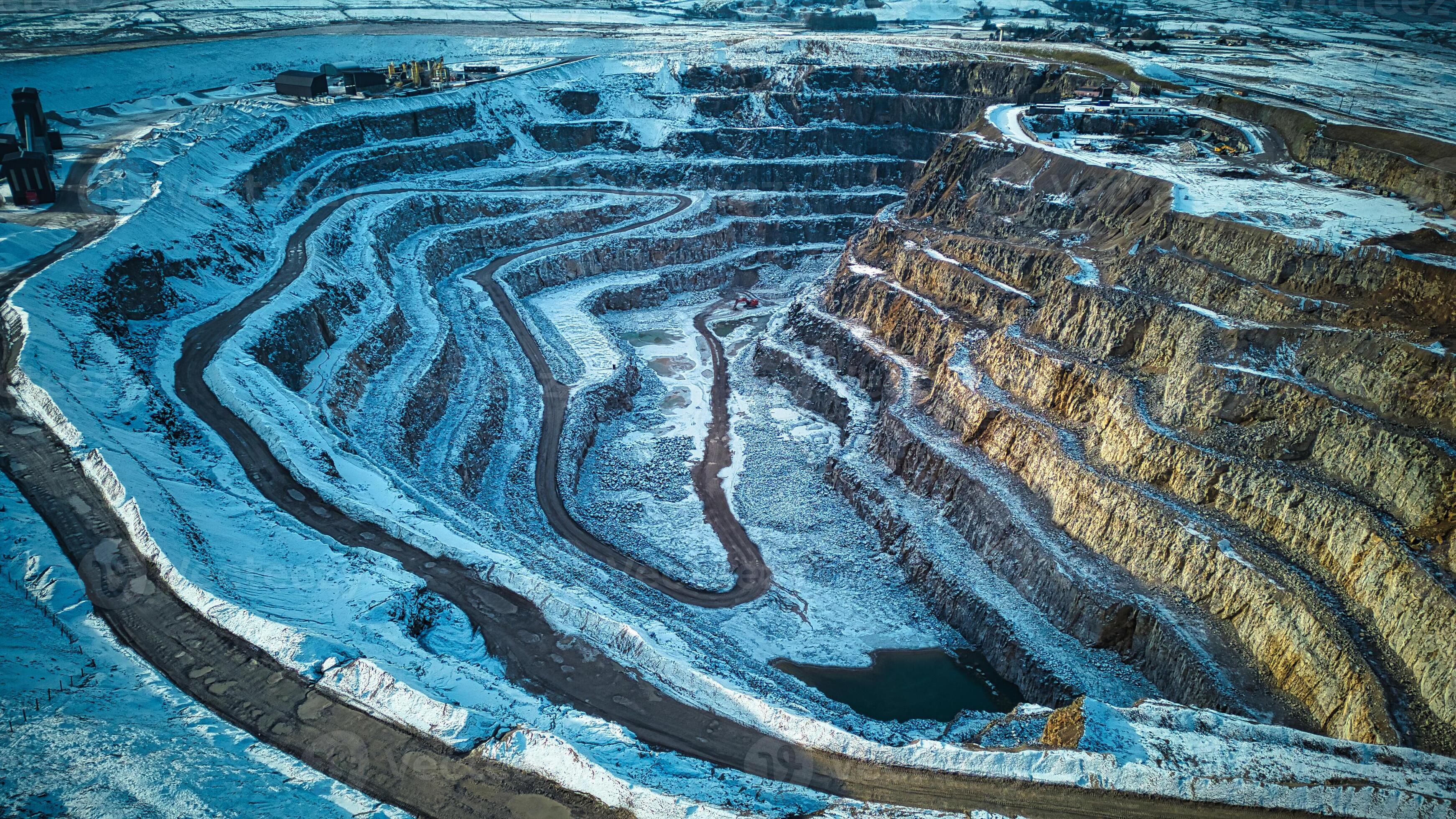 Aerial View Of A Vast Open Pit Mine With Terraced Layers Under A Blue