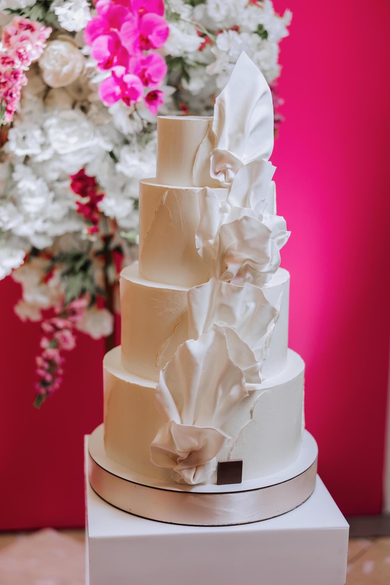 a four-tiered white wedding cake stands on a decorative stand ... a four-tiered white wedding cake stands on a decorative stand ...