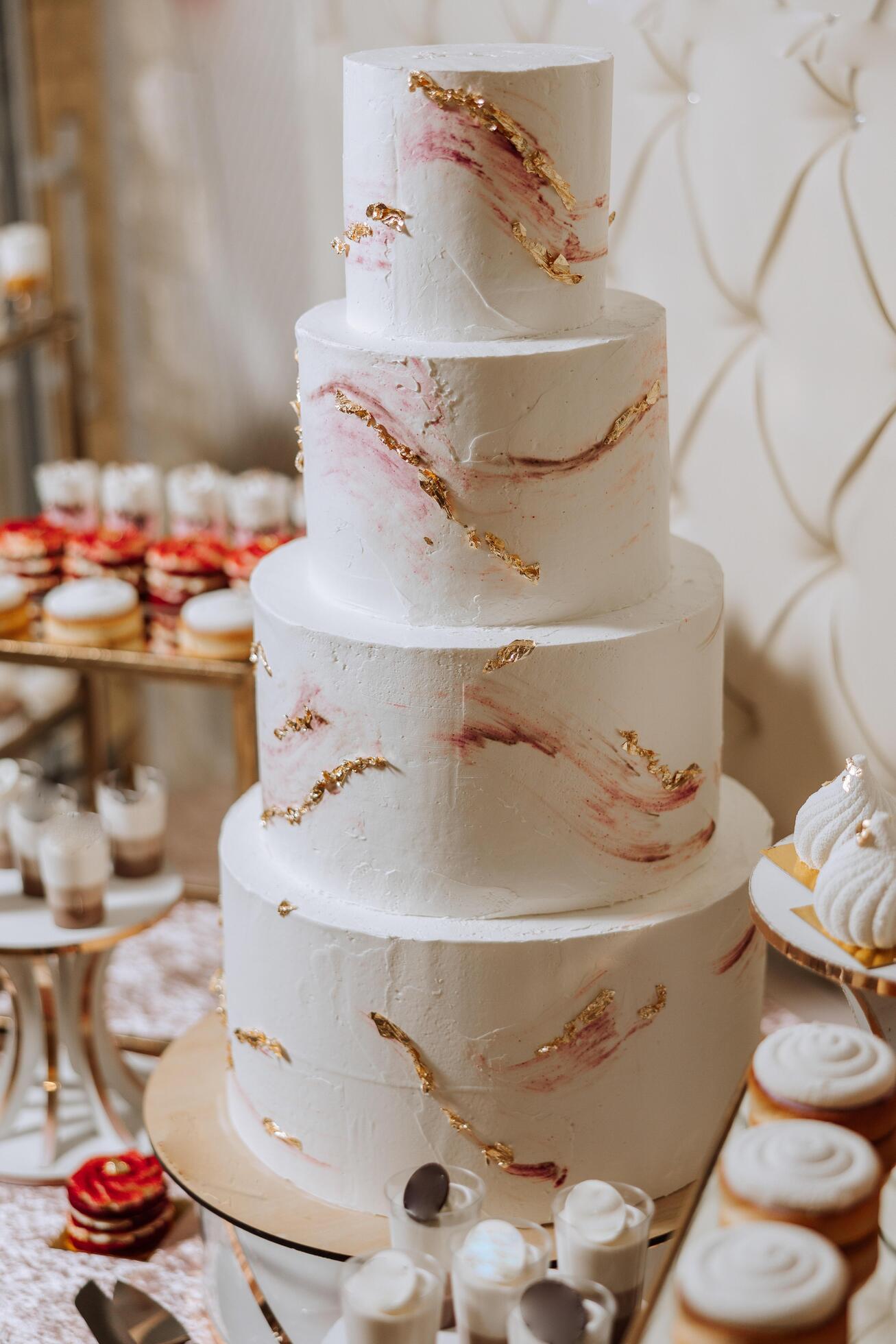 a four-tiered white wedding cake stands on a decorative stand ... a four-tiered white wedding cake stands on a decorative stand ...