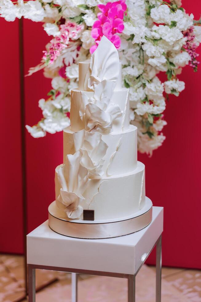 a four-tiered white wedding cake stands on a decorative stand ... a four-tiered white wedding cake stands on a decorative stand ...