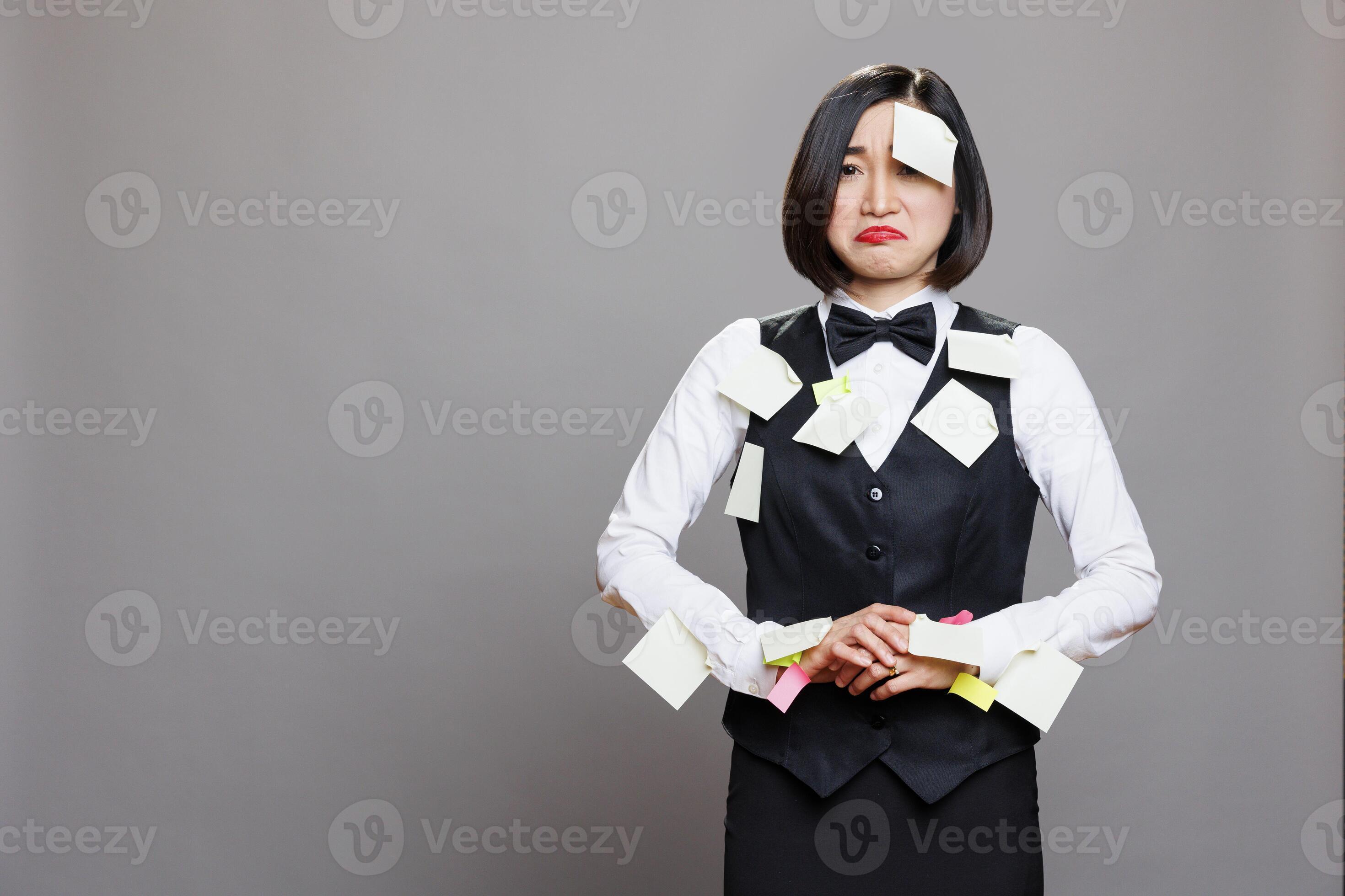 Depressed asian waitress in uniform stressed with workload looking at camera with upset ...