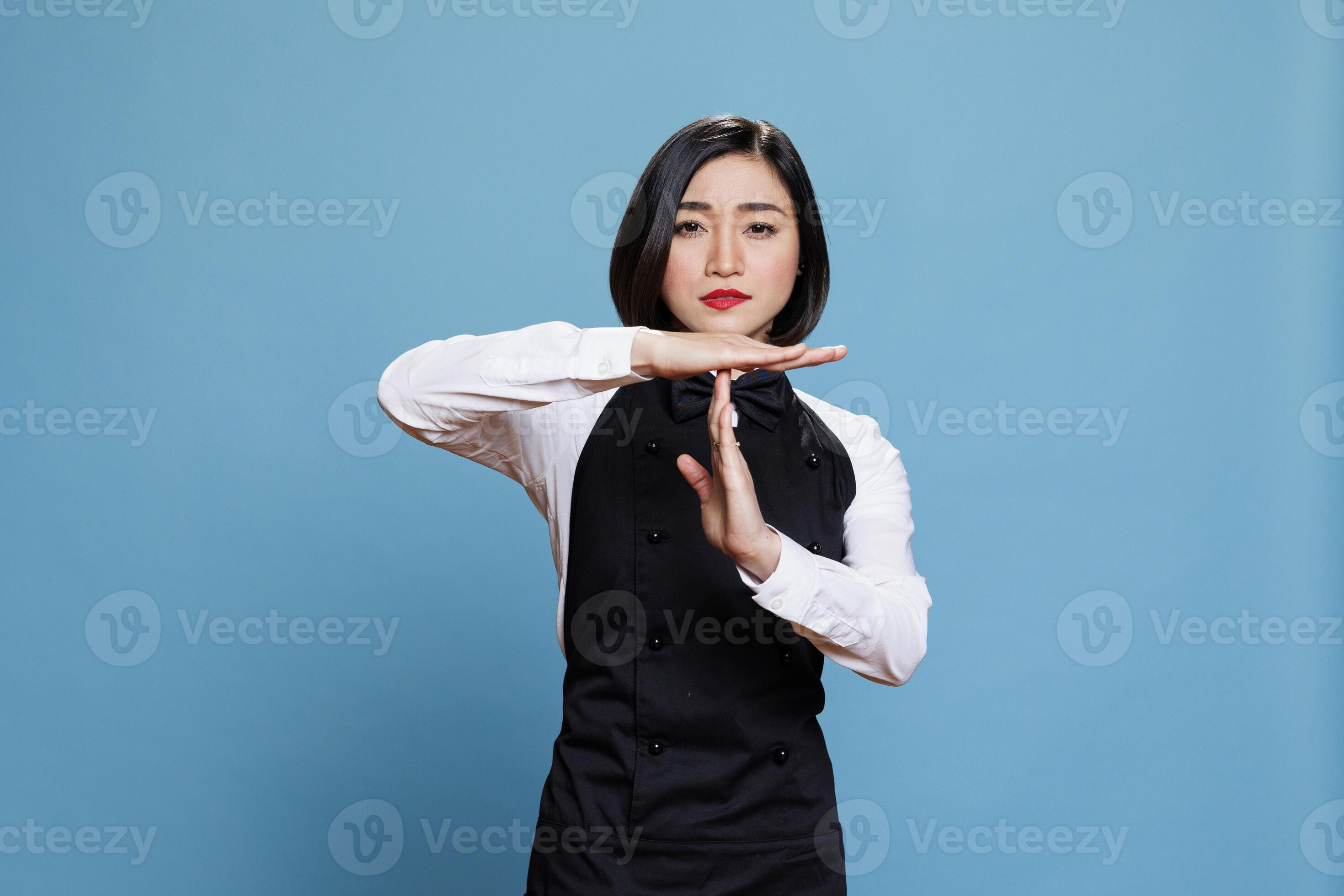 Confident asian waitress dressed in restaurant uniform making timeout gesture with arms portrait ...
