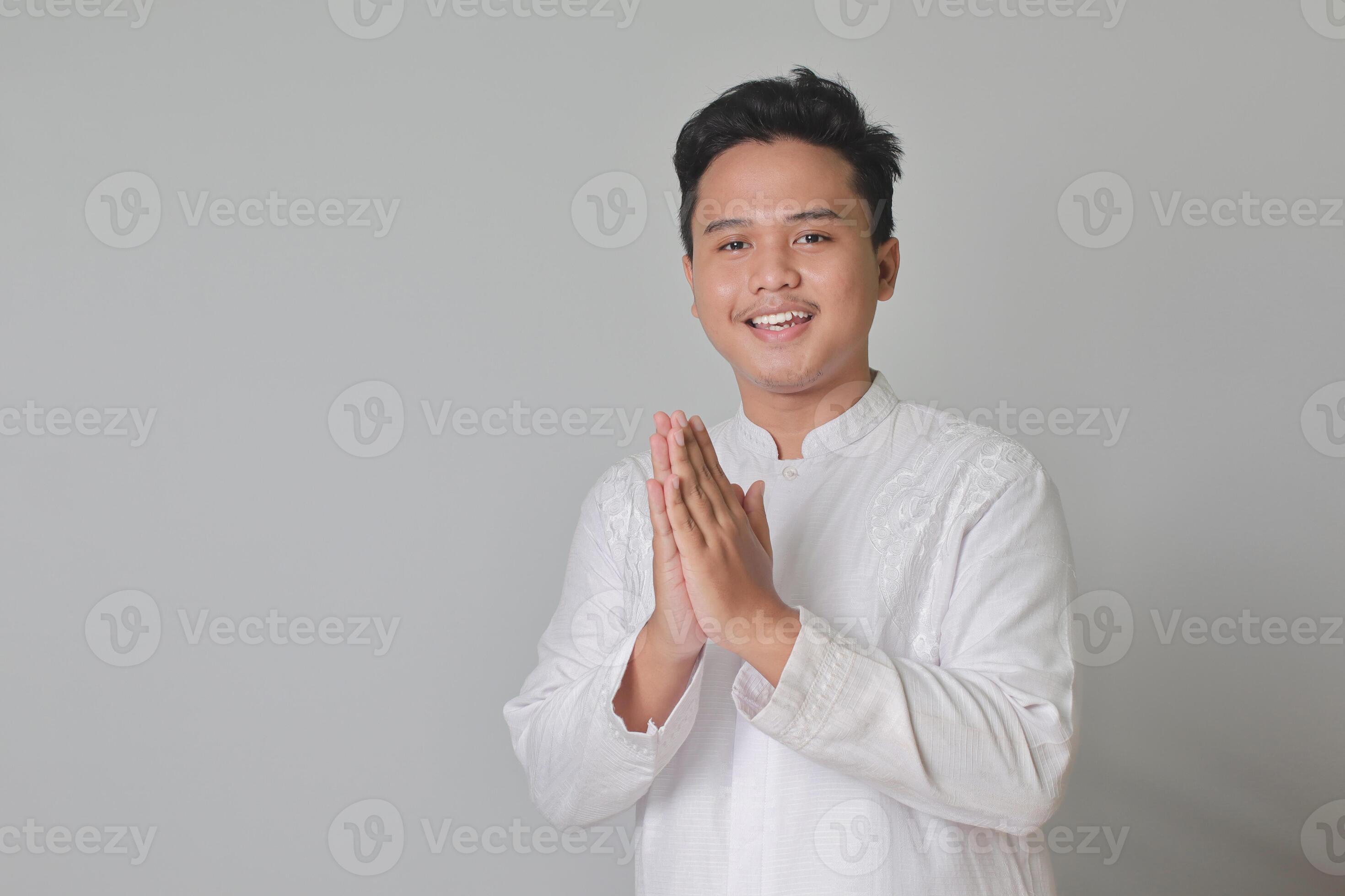 Portrait of Asian muslim man in white koko shirt showing apologize and welcome hand gesture ...