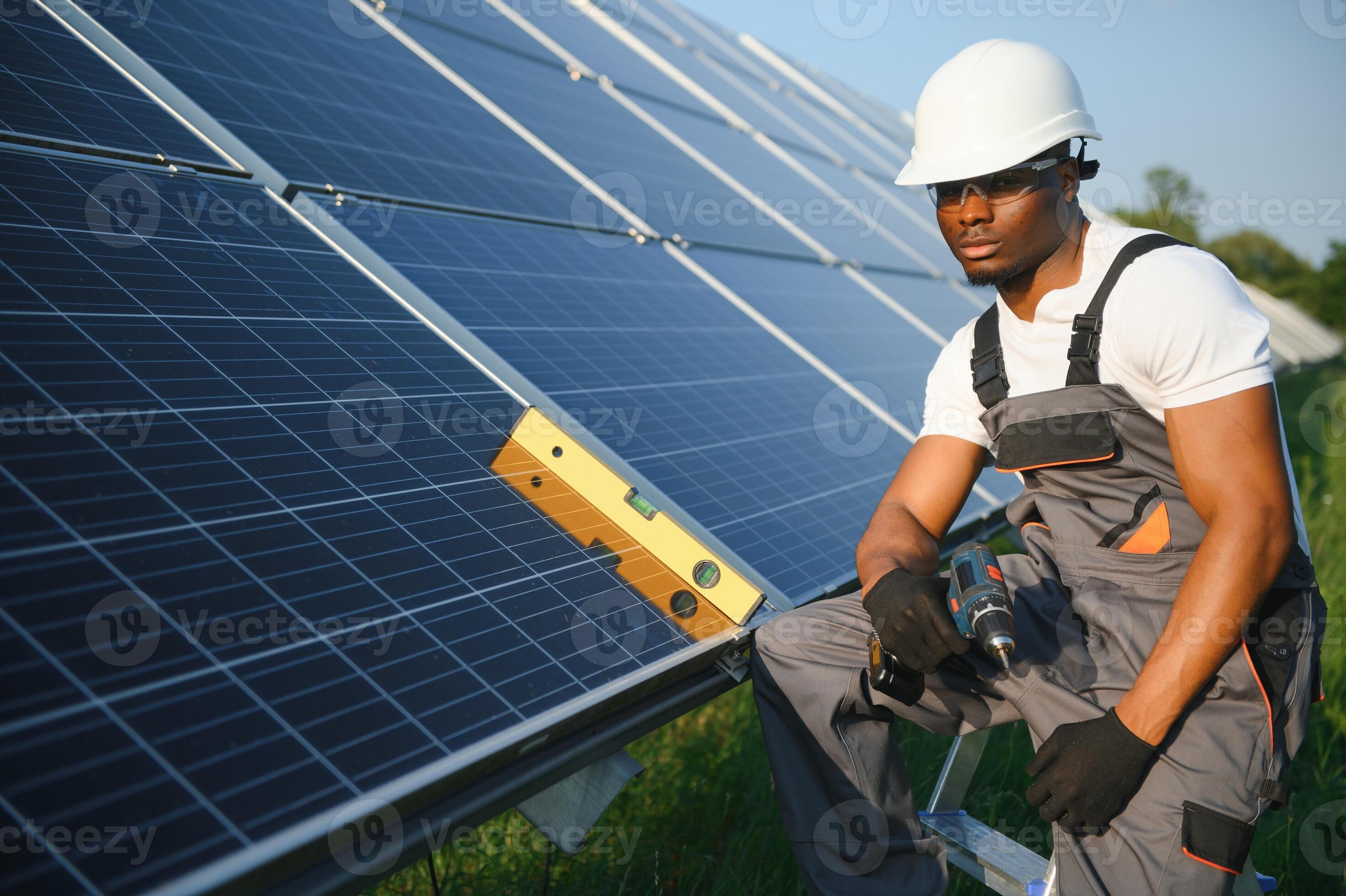 African American Man In Safety Helmet And Glasses Tighten Nuts On Solar Panels With Screwdriver