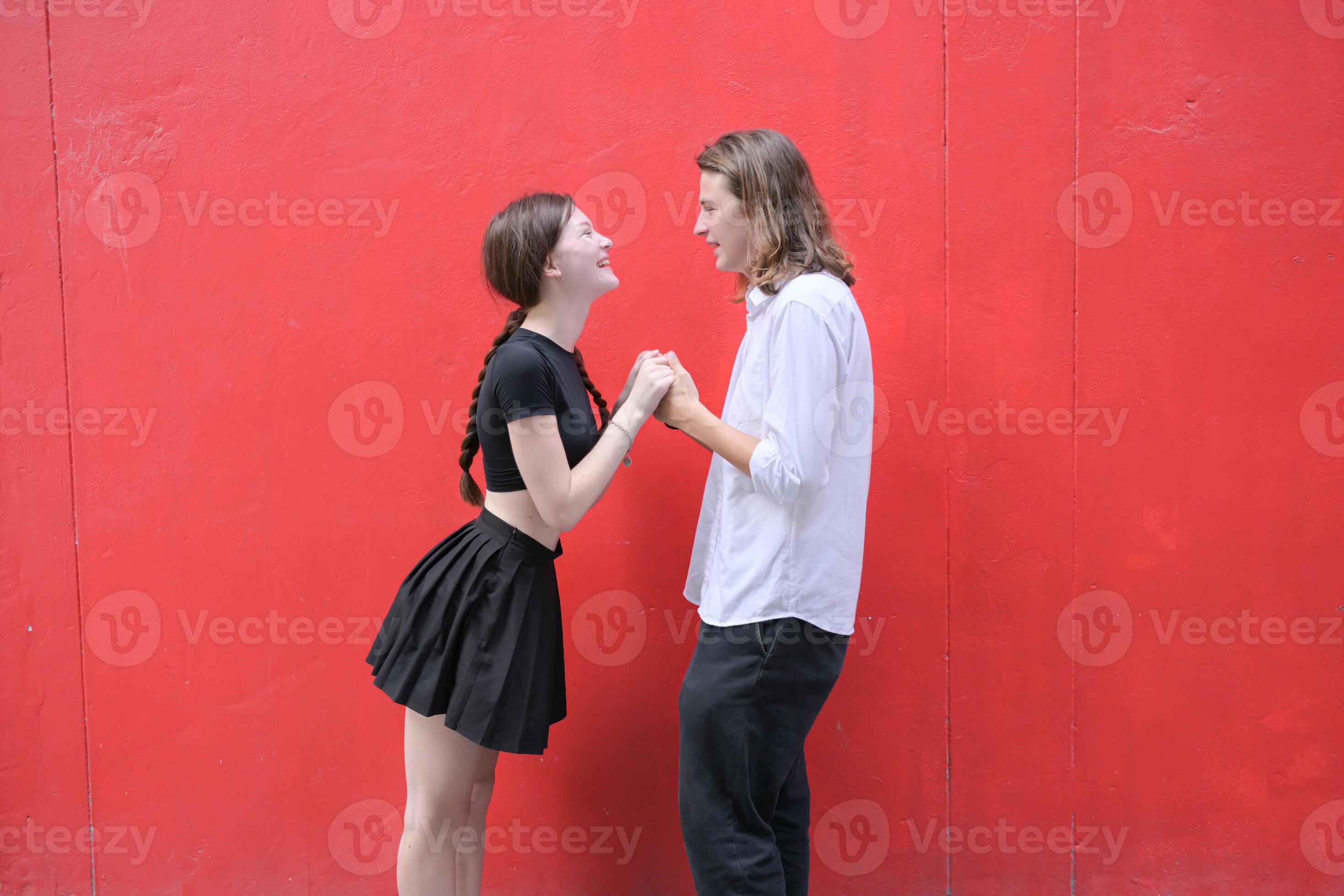 A Couple Is Enjoying A Summer Vacation In The Red Wall Background Happily Showing Their Love To