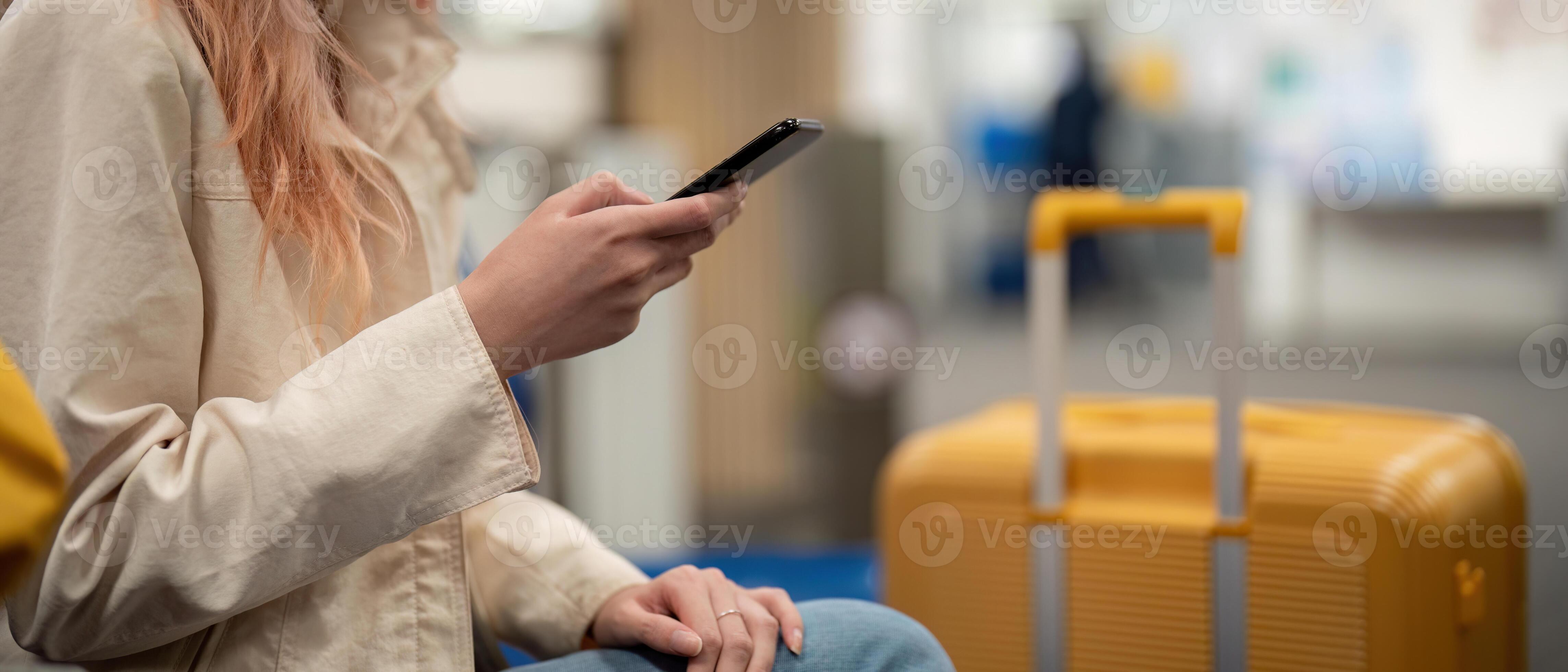 Tourist woman using mobile smartphone with suitcase traveling between waits for flight in ...