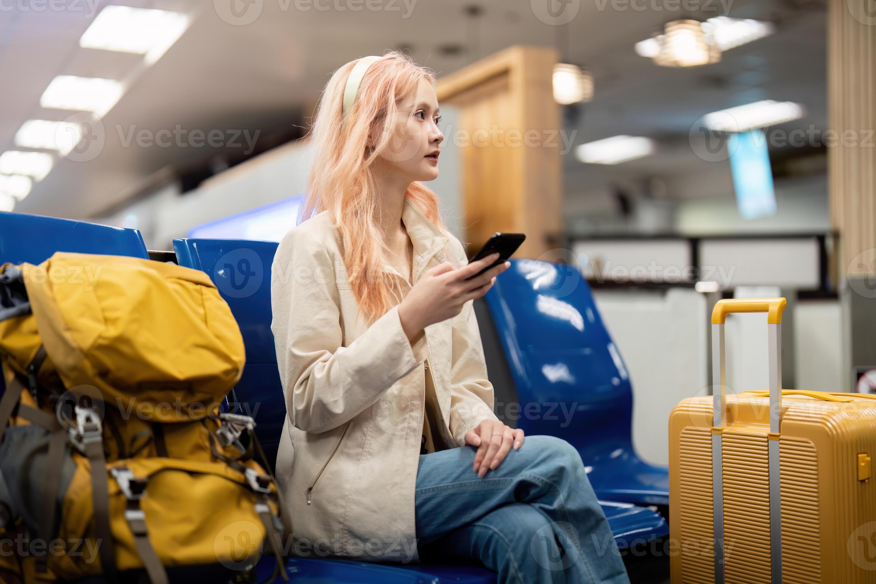 Happy asian tourist woman using mobile smartphone with suitcase traveling between waits for ...