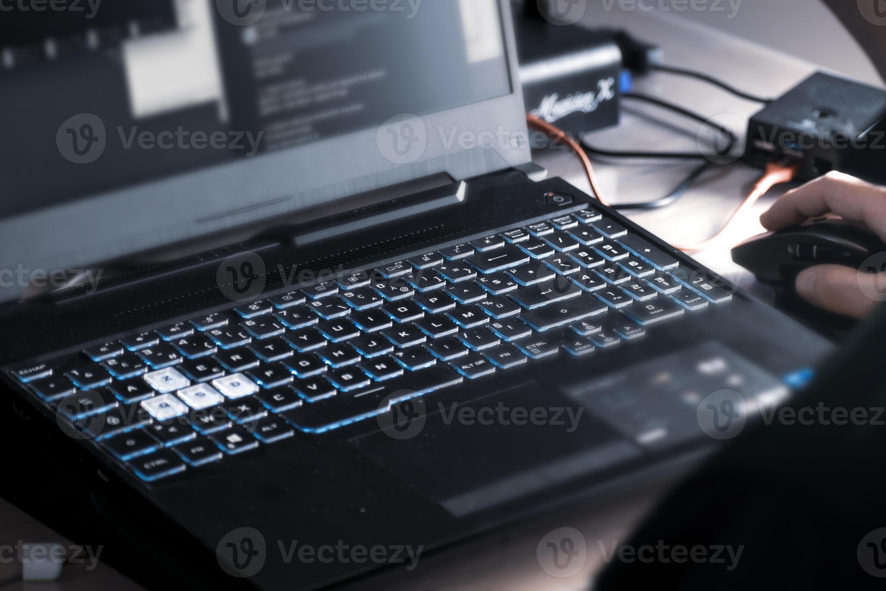 Close up of man's hand using wireless mouse and laptop computer with blue backlit keyboard ...