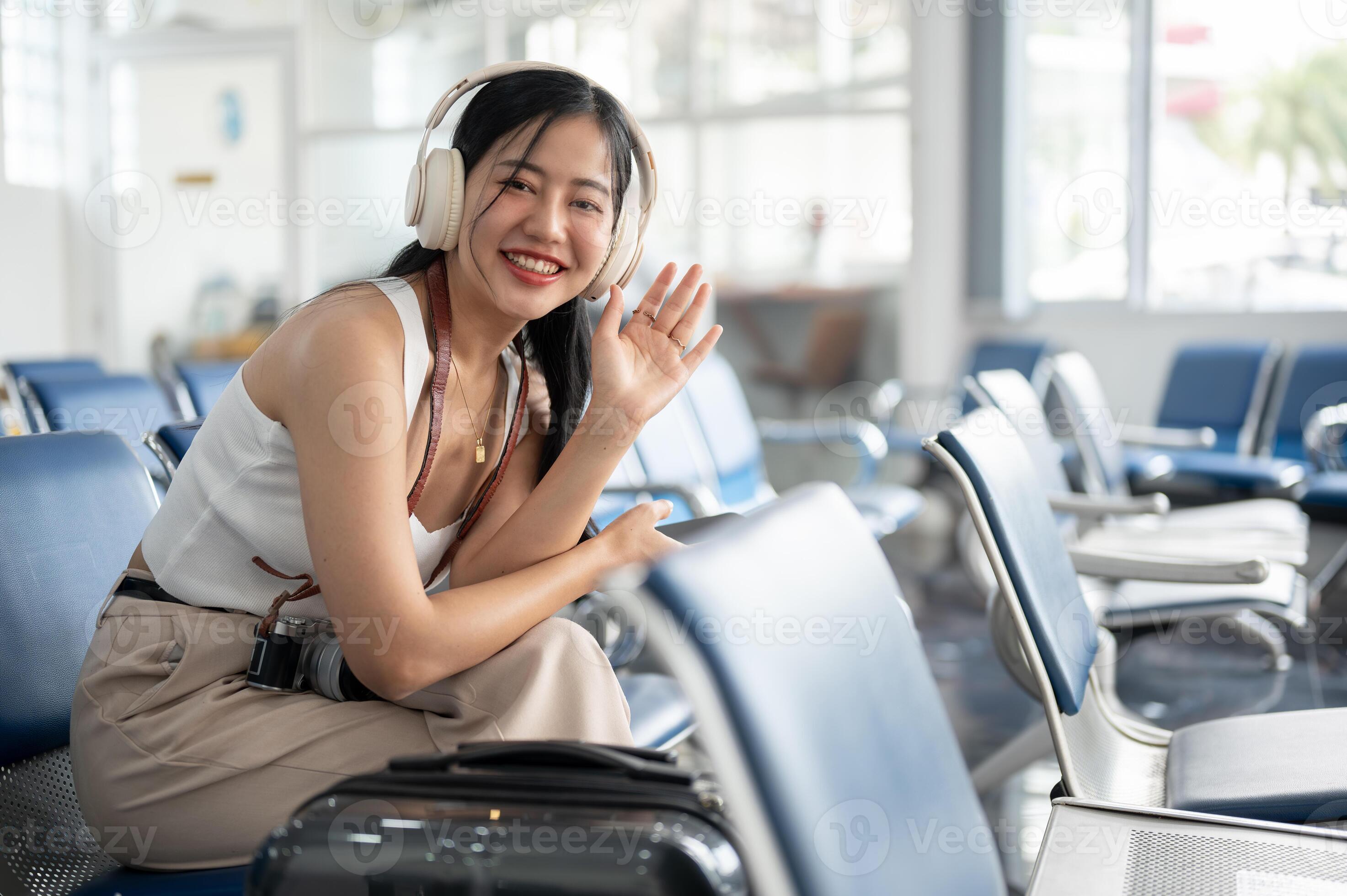 An attractive Asian female traveler passenger is sitting in the airport terminal, travel by ...