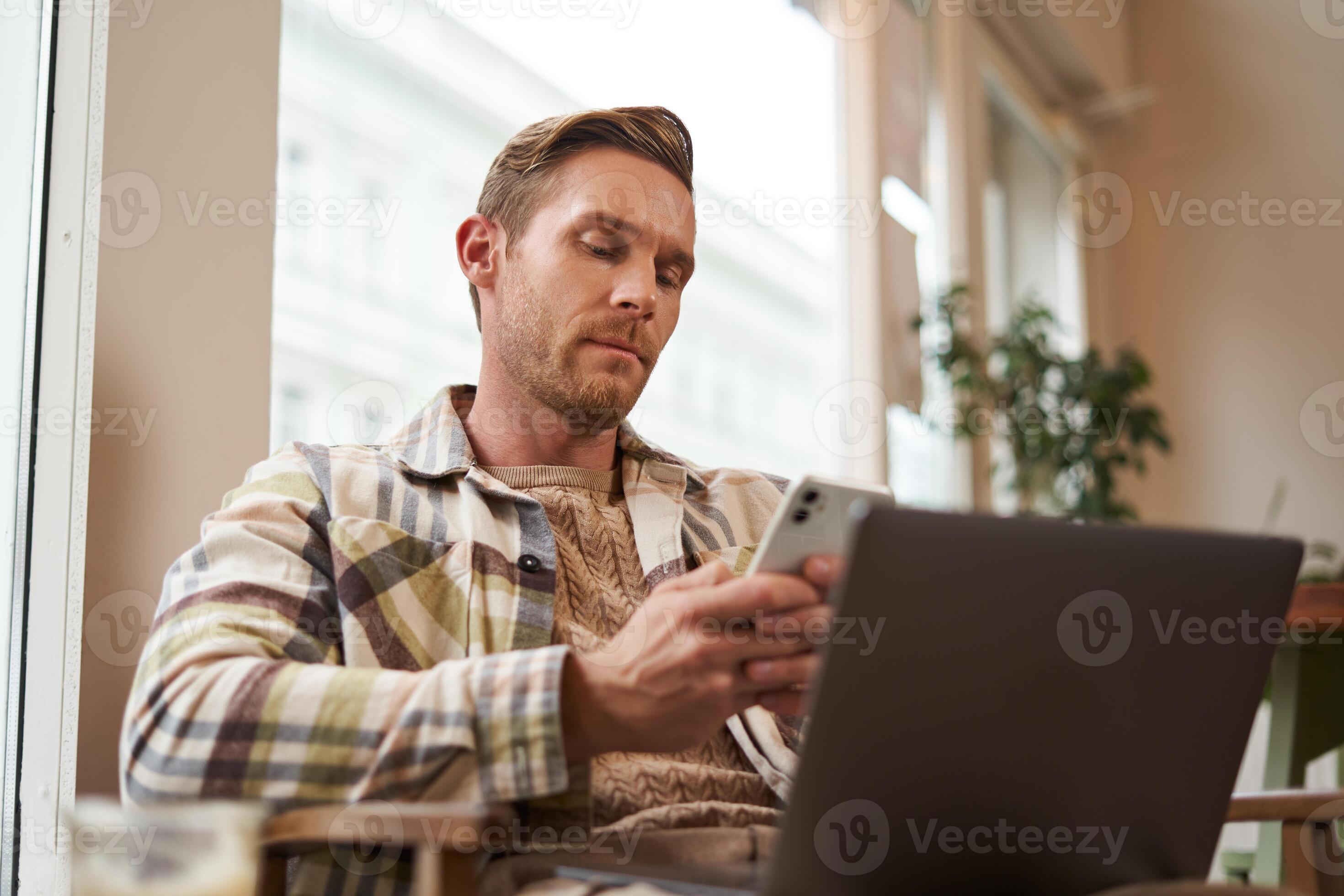 Portrait of man with serious face, scrolling news feed on mobile phone, looking concentrated at ...