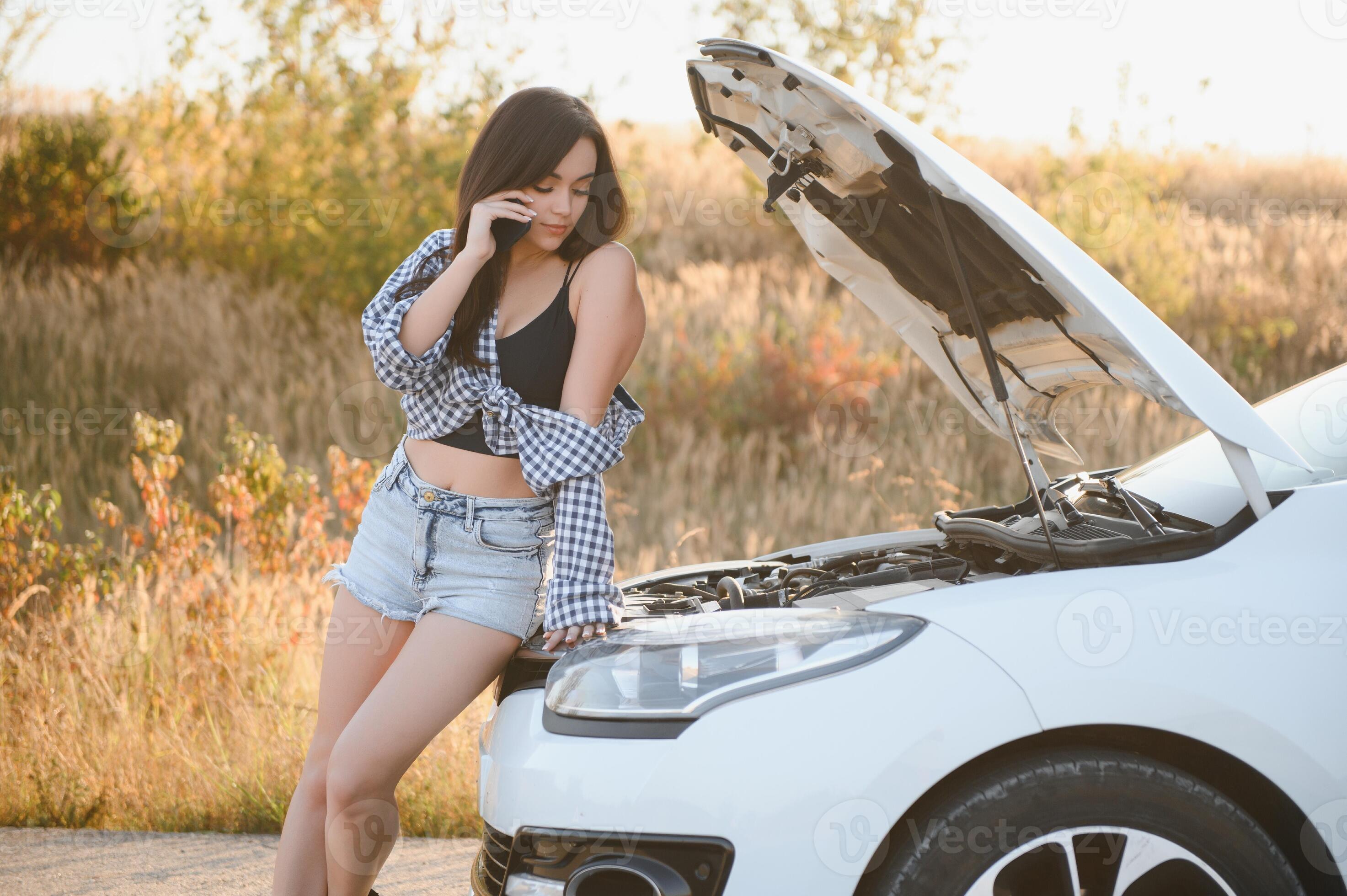 The young girl broke the car and she opened the hood and tried to repair the car on the road. A ...