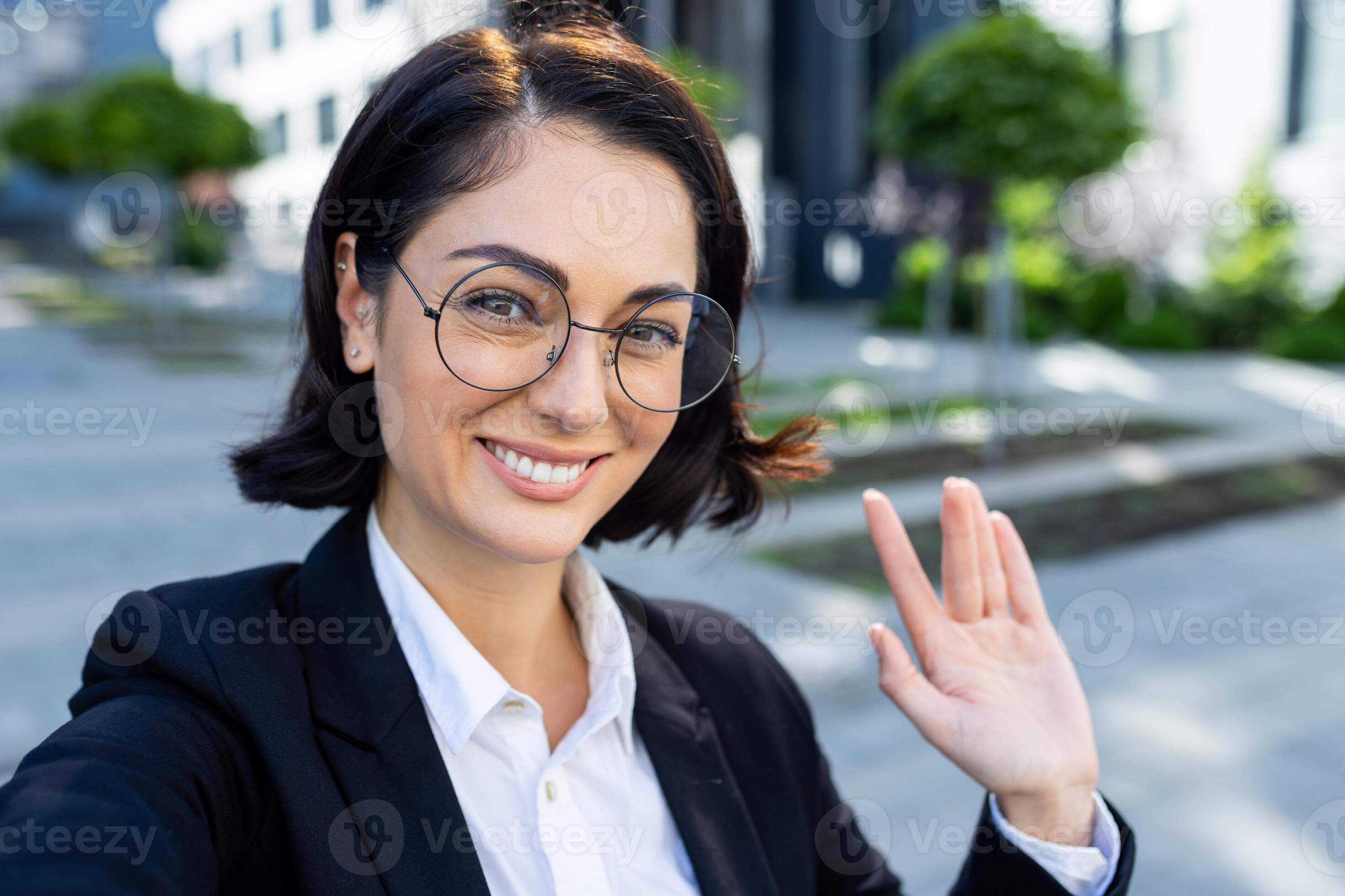 Smiling Professional Woman With Glasses Waving At The Camera Making A Friendly Gesture During A