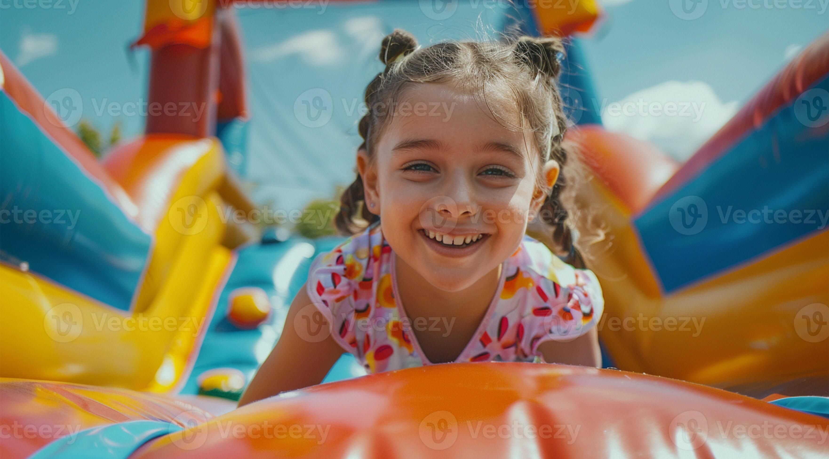 Little girl having fun on an inflatable bouncy castle, with her family watching in the ...