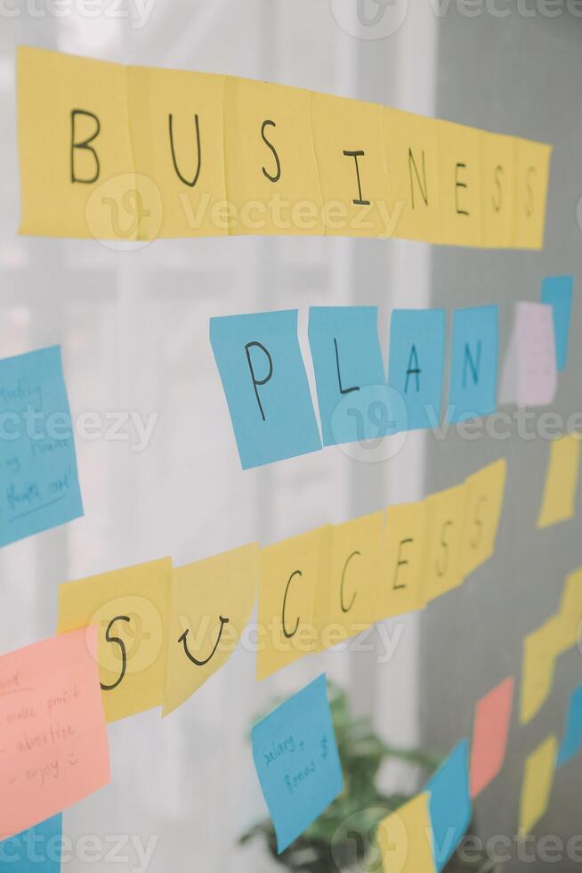 Young creative team professional using post it notes in glass wall to ...