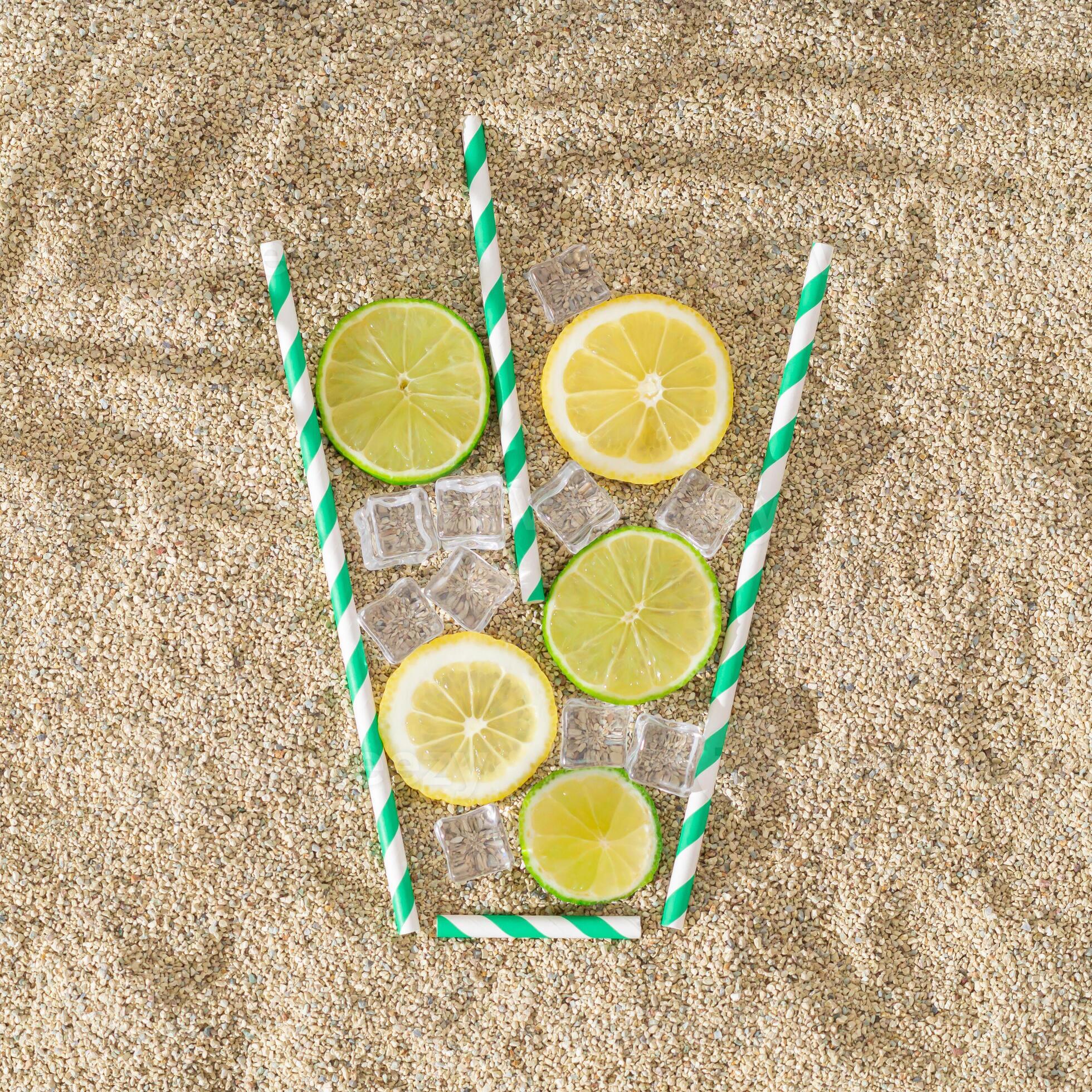 Creative summer composition with lemon and lime slices, drinking straw and ice cubes on sandy ...