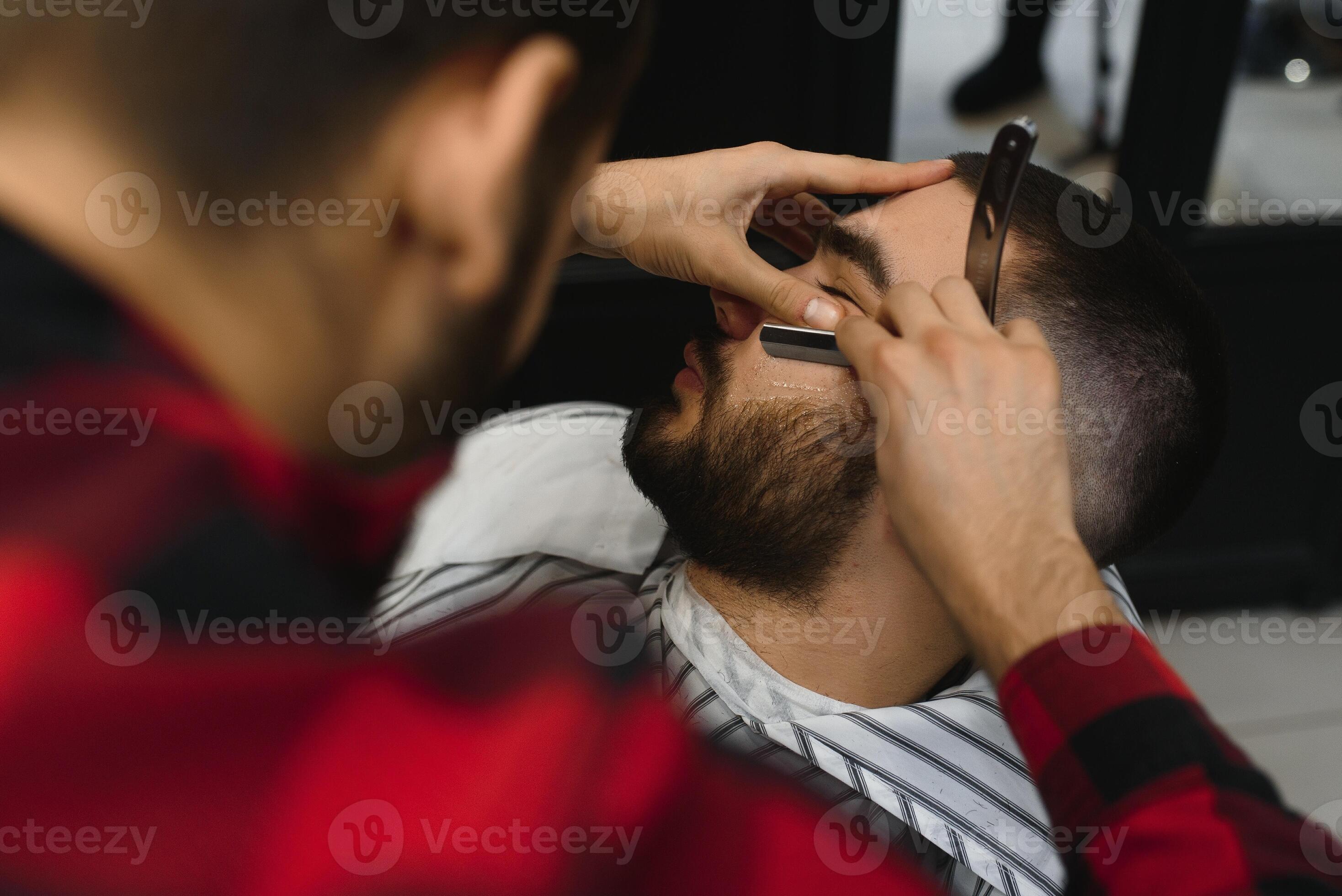 Serious Bearded Man Getting Beard Haircut With A Straight Razor By Barber While Sitting In Chair ...