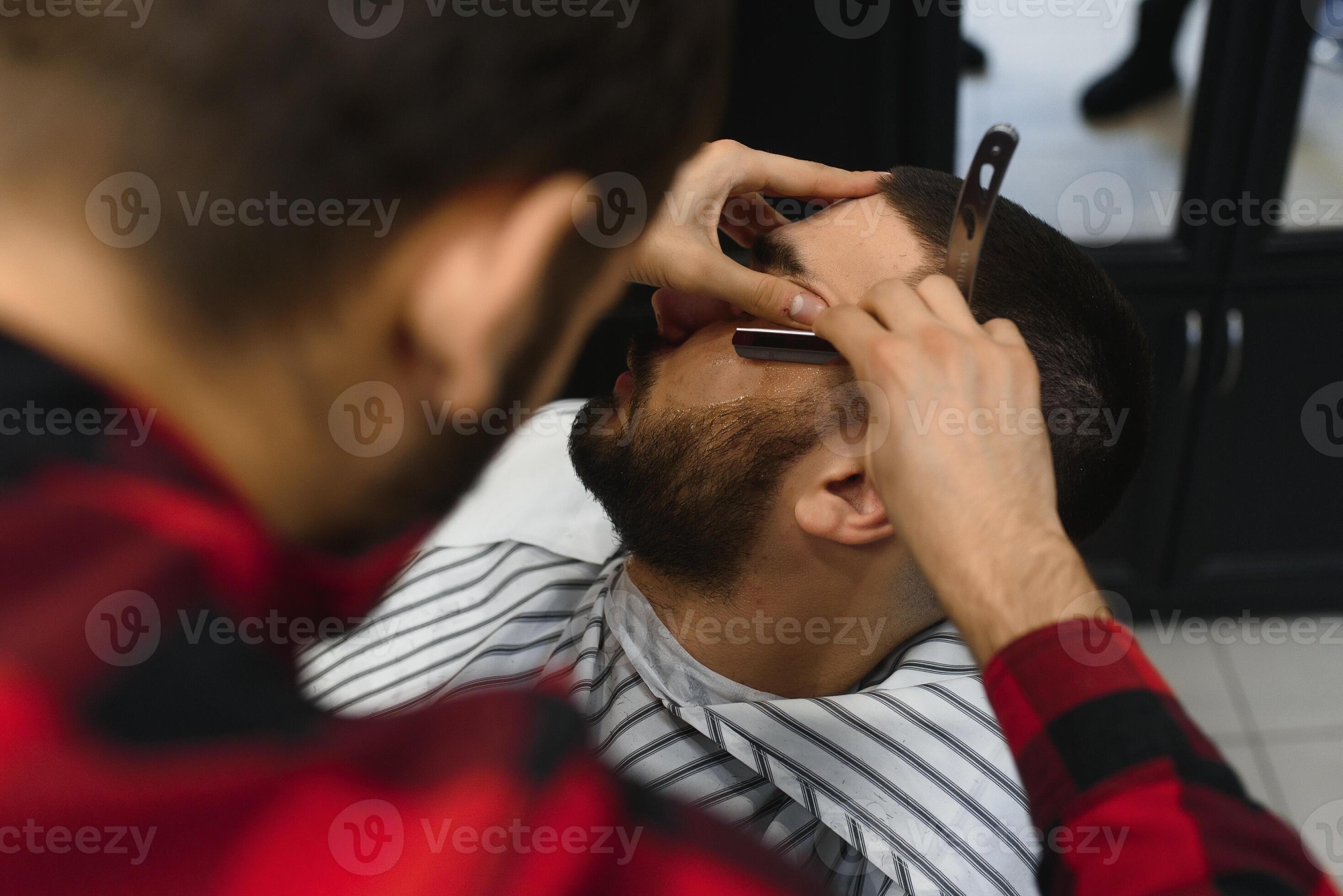 Serious Bearded Man Getting Beard Haircut With A Straight Razor By Barber While Sitting In Chair ...