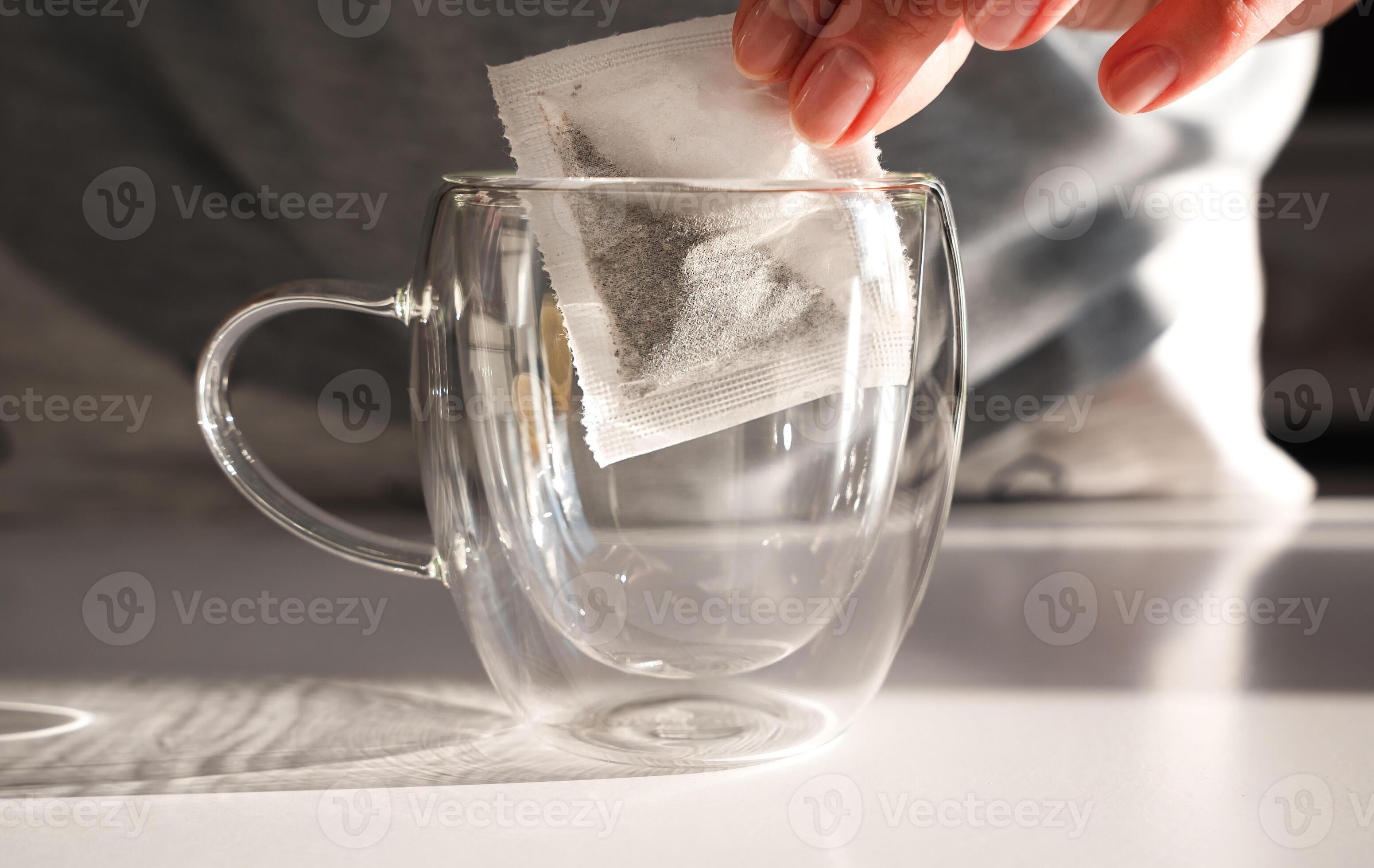 A woman's hand puts a tea bag in a cup. Tea drinking concept. Close-up. Selective focus ...