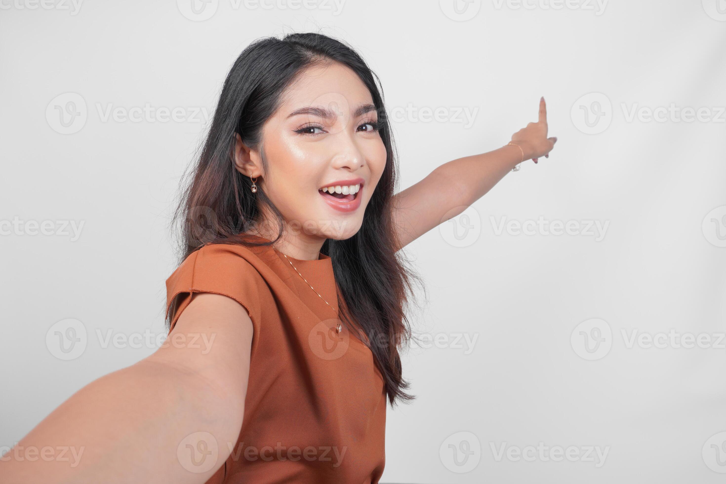 Smiling young Asian woman in brown t-shirt doing call pose while pointing to the copy space ...