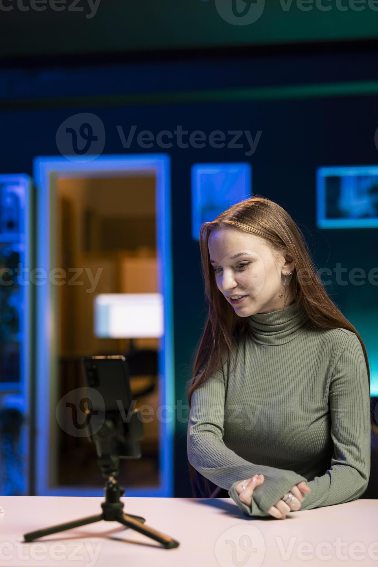 Smiling gen Z content creator utilizes smartphone on tripod to shoot introductory segment for ...