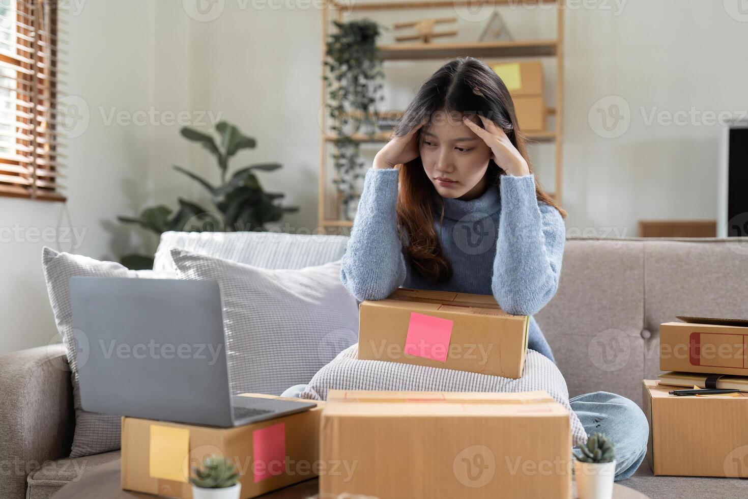 Stressed woman working with laptop computer and courier parcel box at home office. SME online ...