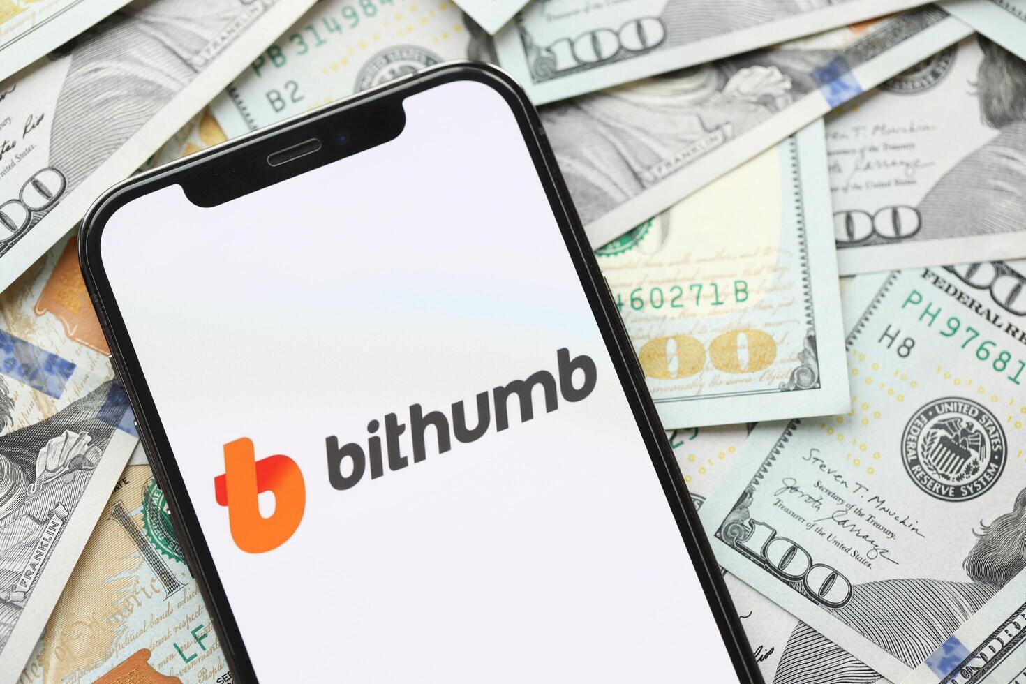 KYIV, UKRAINE - MARCH 15, 2024 Bithumb logo on iPhone display screen with many hundred dollar ...
