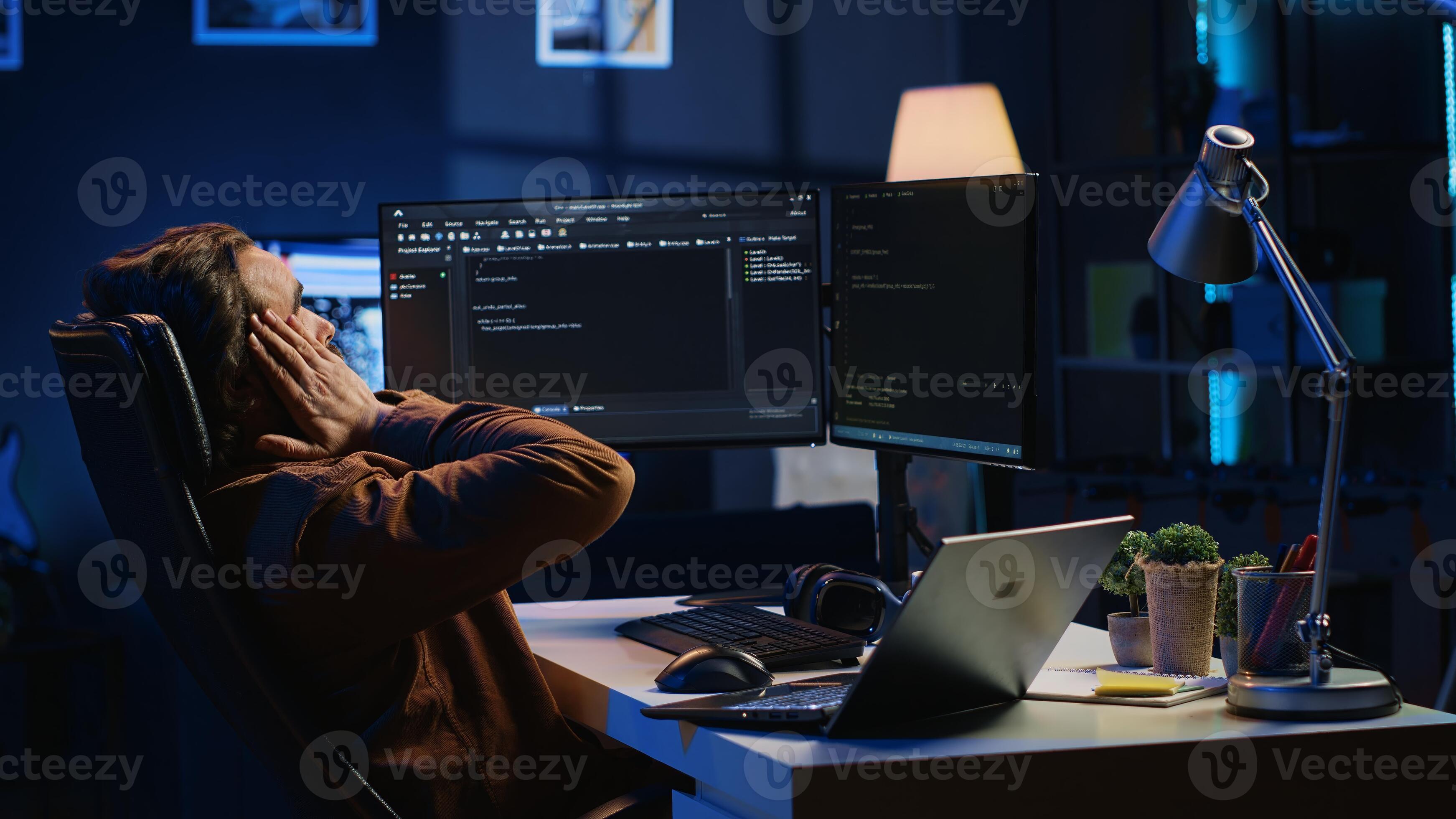 Fatigued software programmer working overnight at home, taking break from coding to stretch at ...