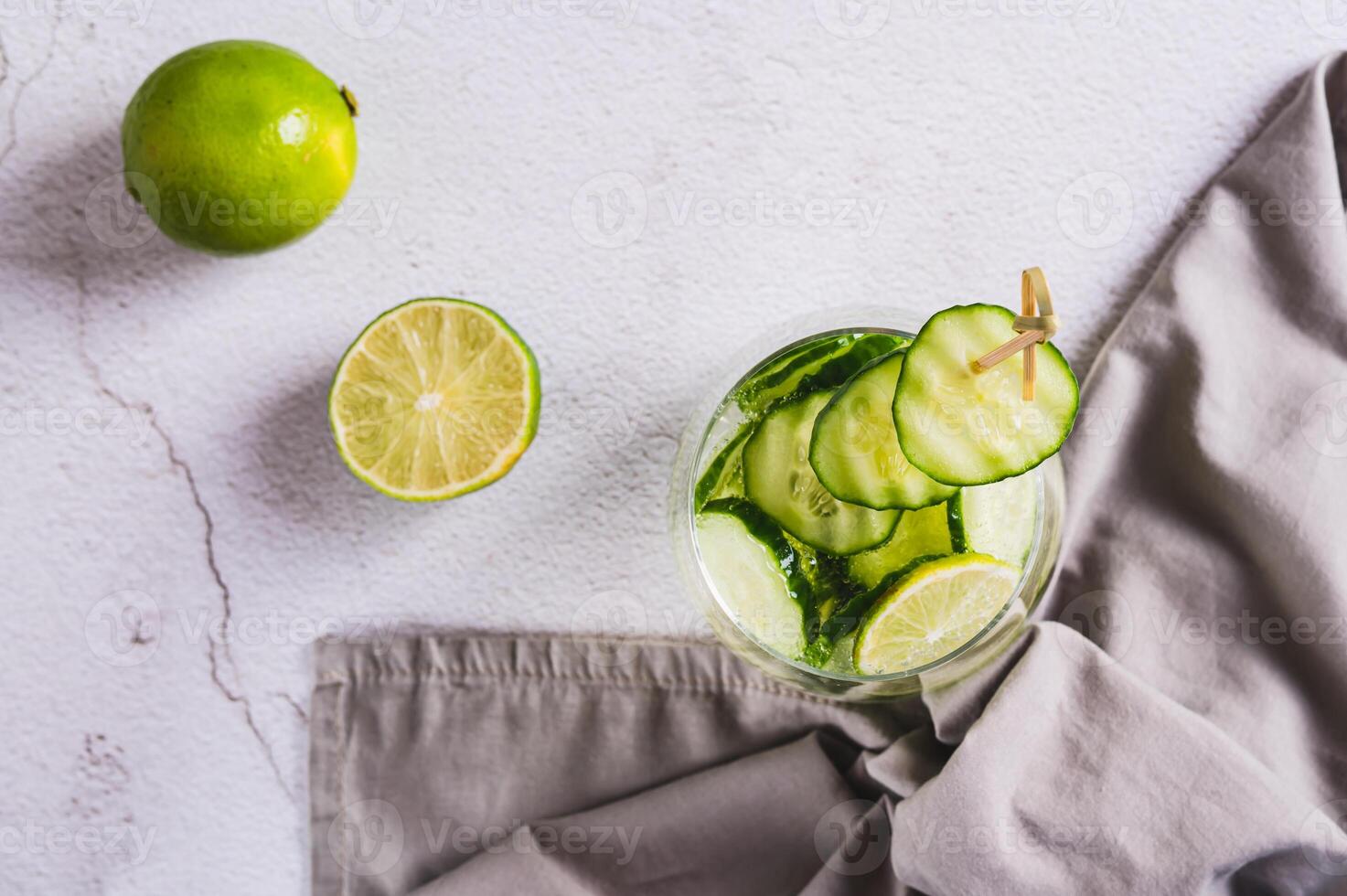 Close up of refreshing carbonated lemonade with lime and cucumber in a glass on the table top ...