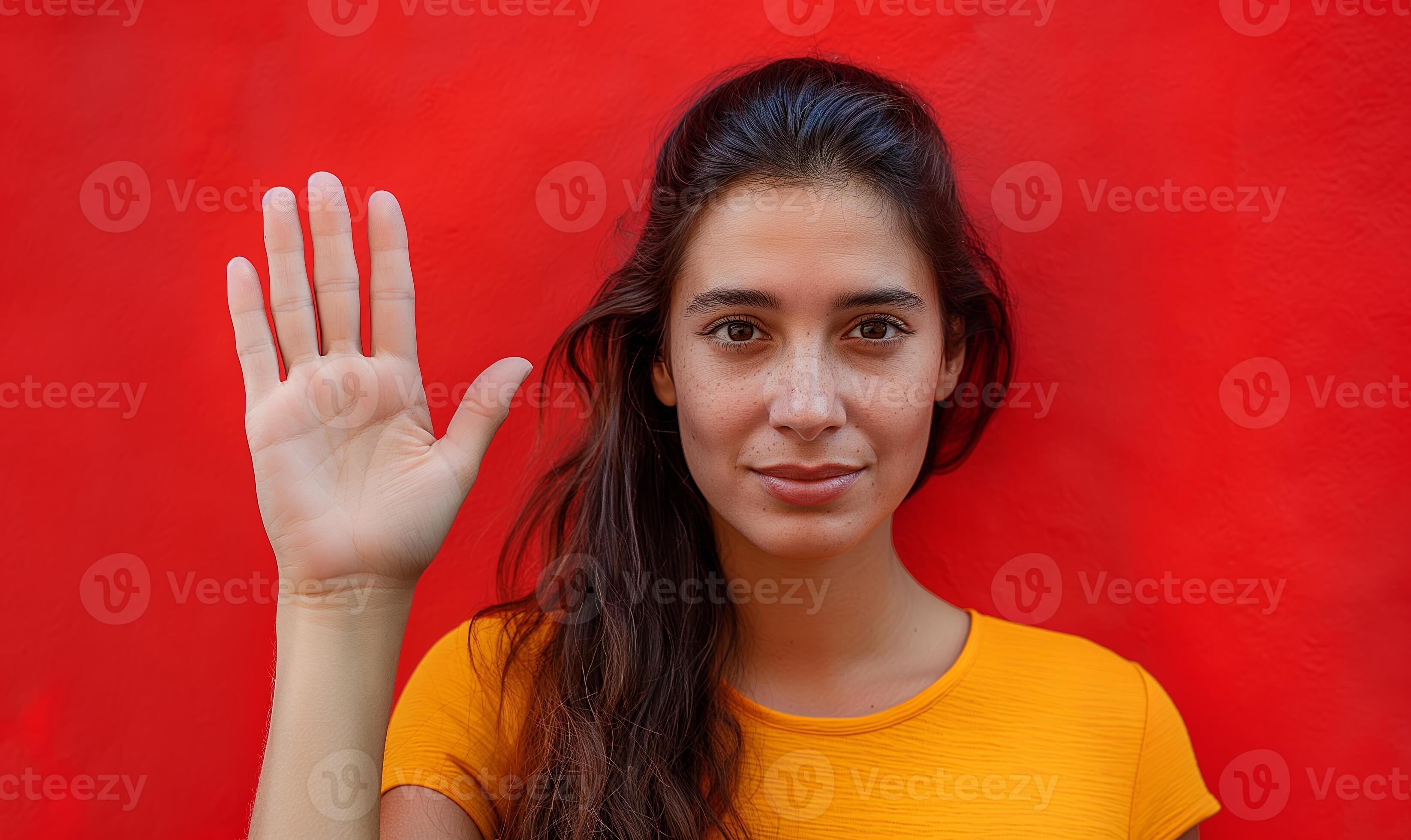 Woman Wearing Yellow Shirt Against Bright Red Wall Raising Hand in Friendly Gesture, Strong ...
