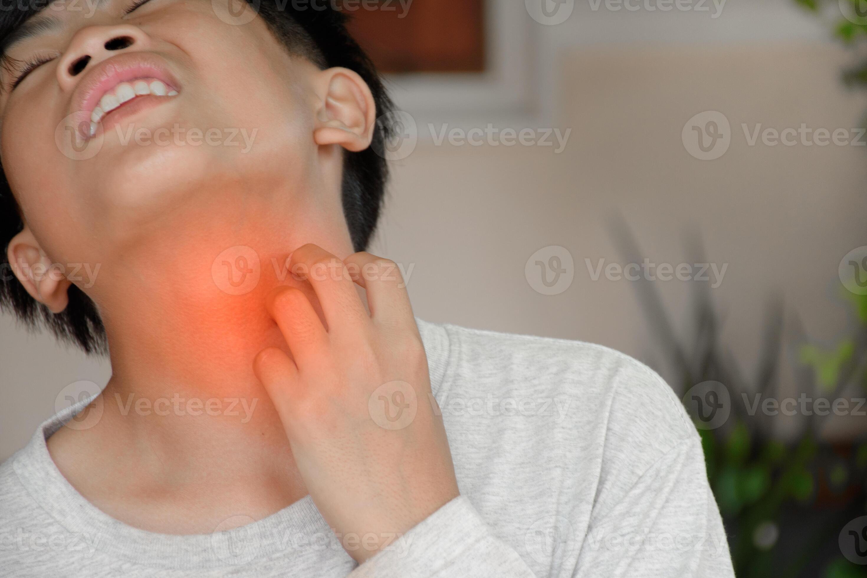Asian young man touching his neck and showing a pained expression due to a sore throat or an ...
