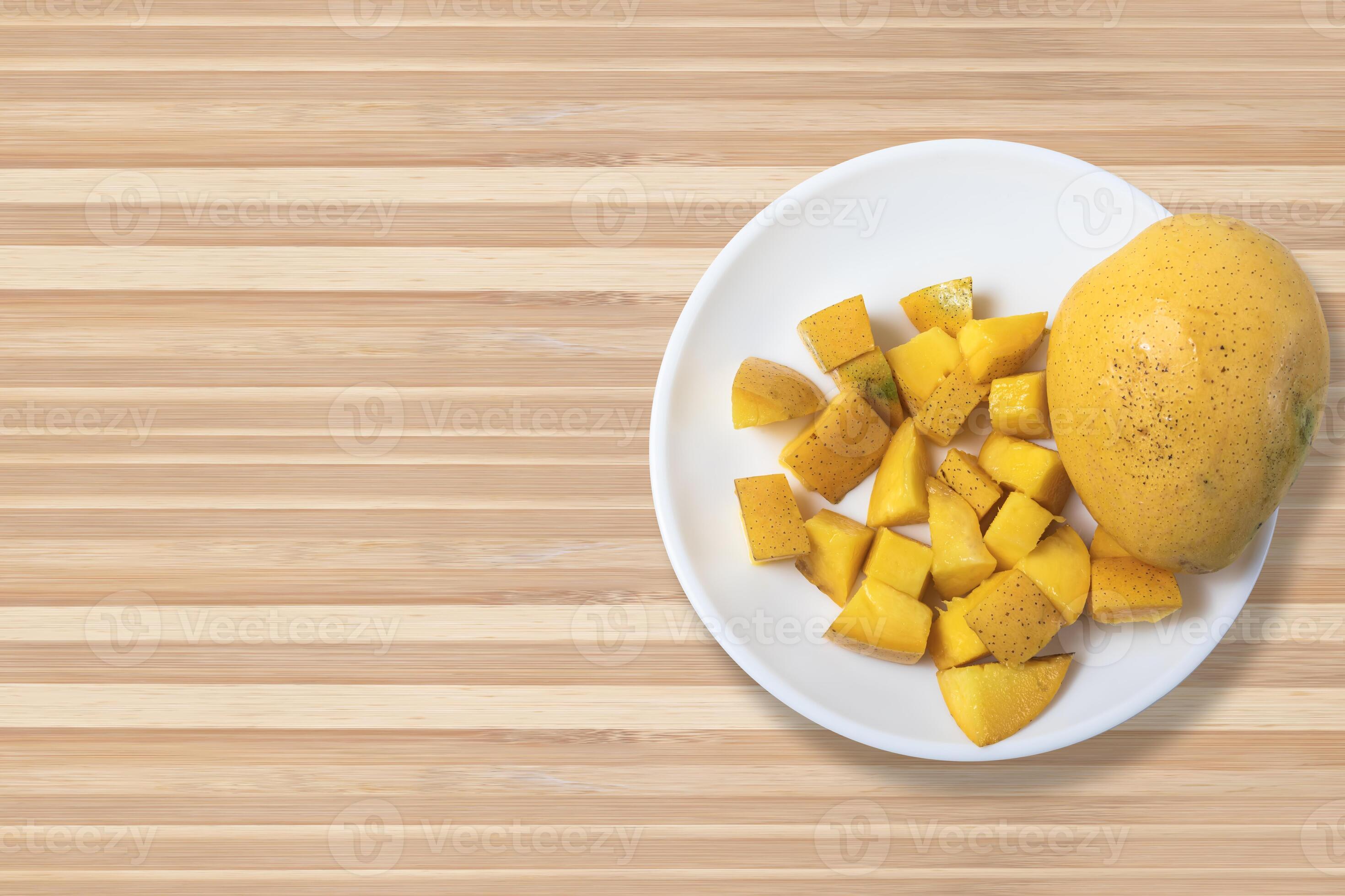Ripe mangoes with sliced mangoes on white plate on wooden table. Healthy food concept. 47110492 ...
