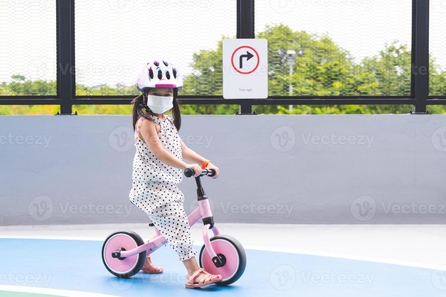 asiático niña disfrutando montando un rosado equilibrar bicicleta, niño vistiendo un casco, con ...
