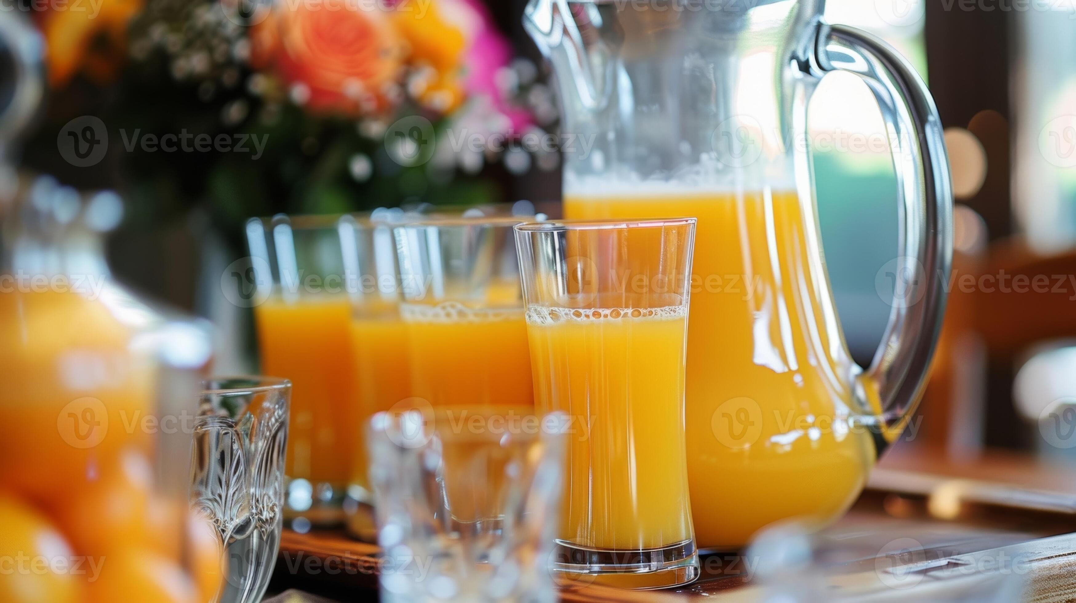 A glass pitcher is filled with freshly squeezed orange juice ready to be poured into delicate ...