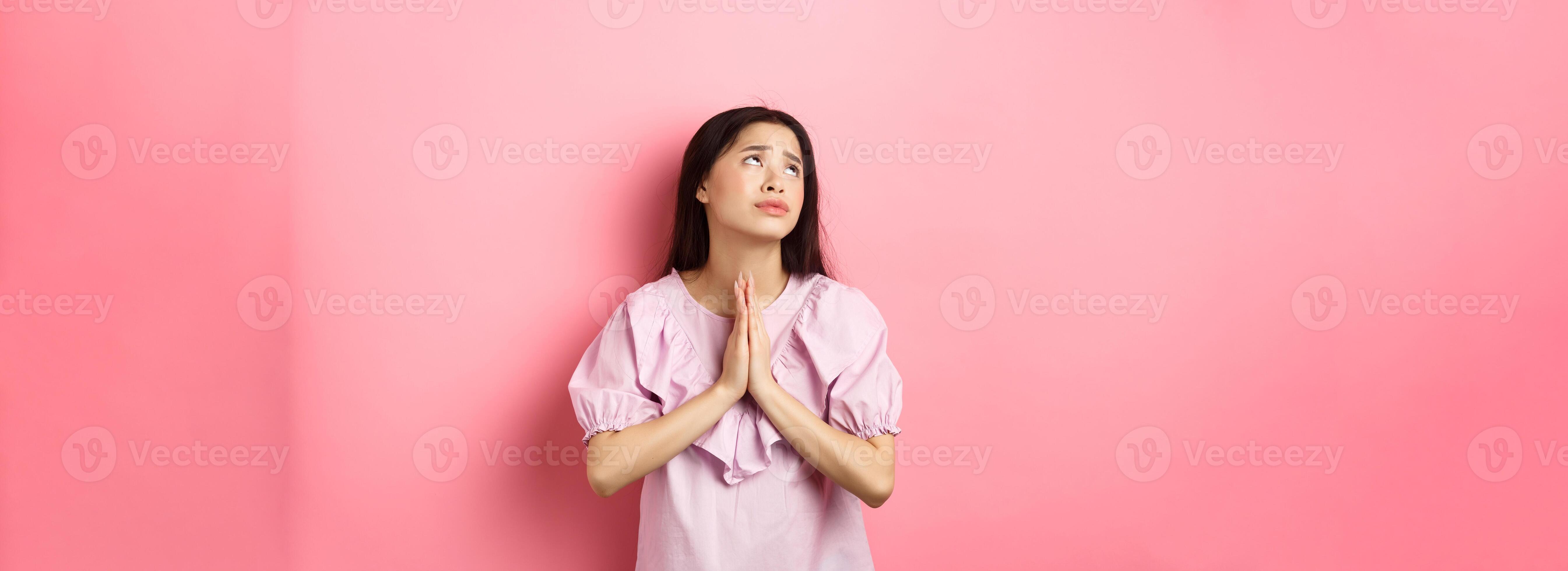 Hopeful asian girl praying god, looking up to plead or pray, making wish, supplicating with ...