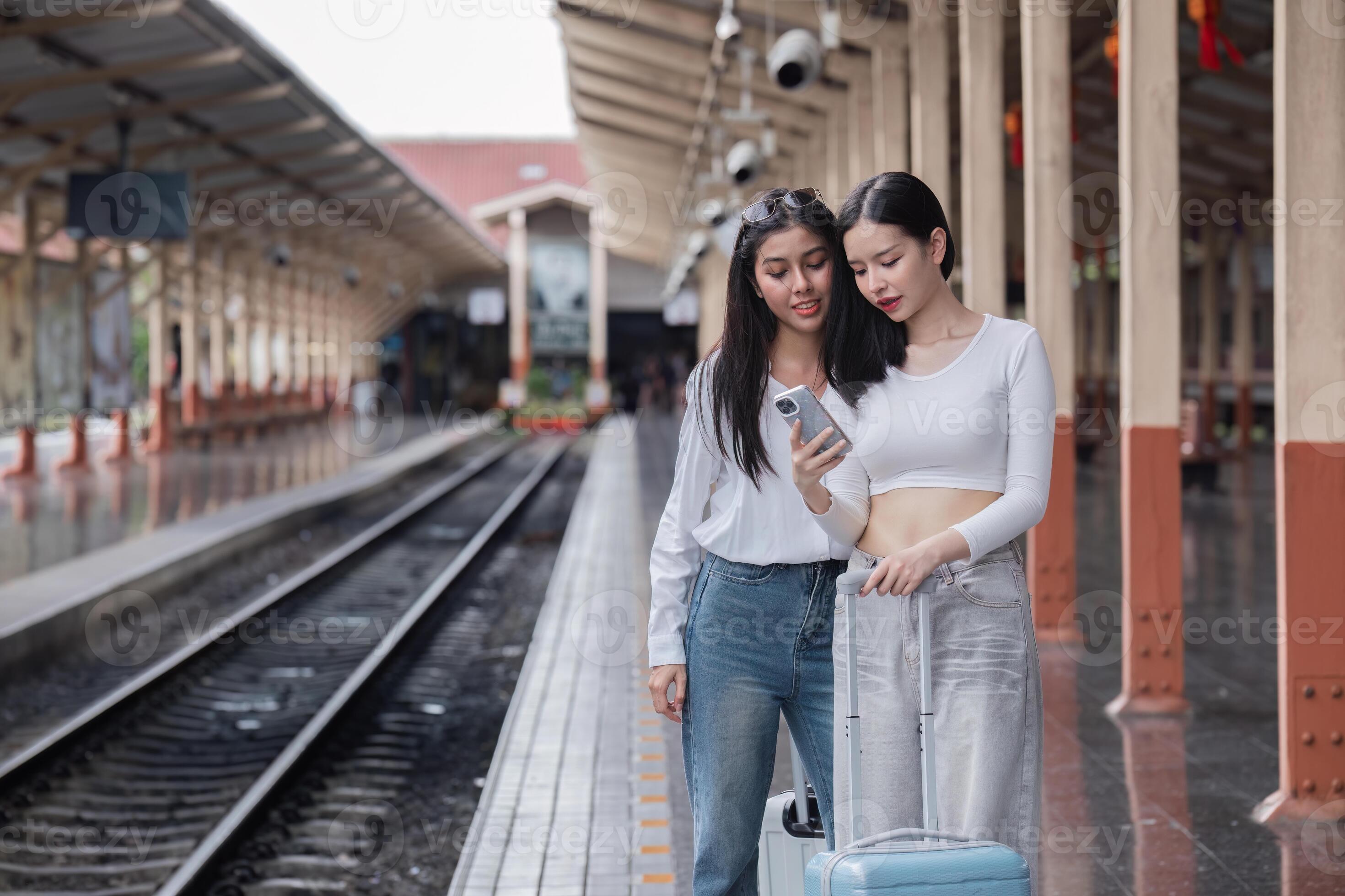 Young Female Friends Waiting for the Train Together at the Station, Checking Phone and Luggage ...