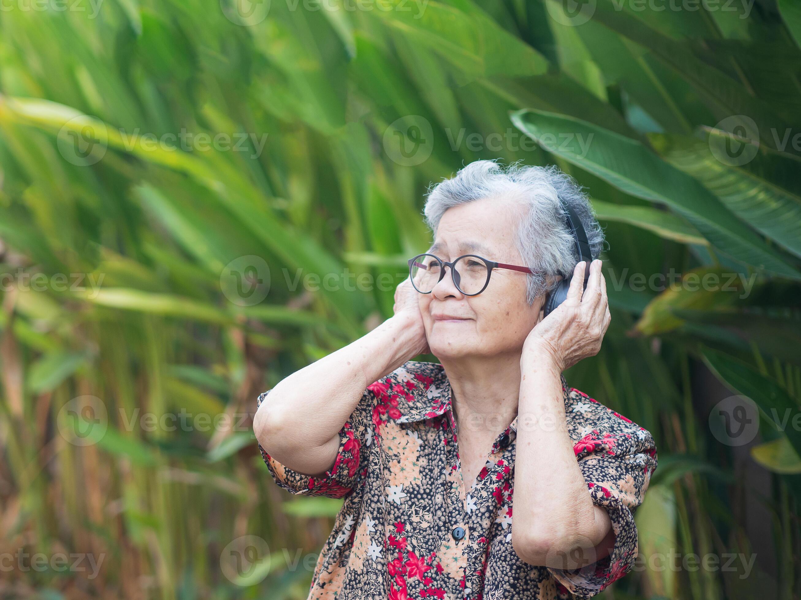Cheerful senior woman with short gray hair, wearing glasses, smiling, and wearing wireless ...