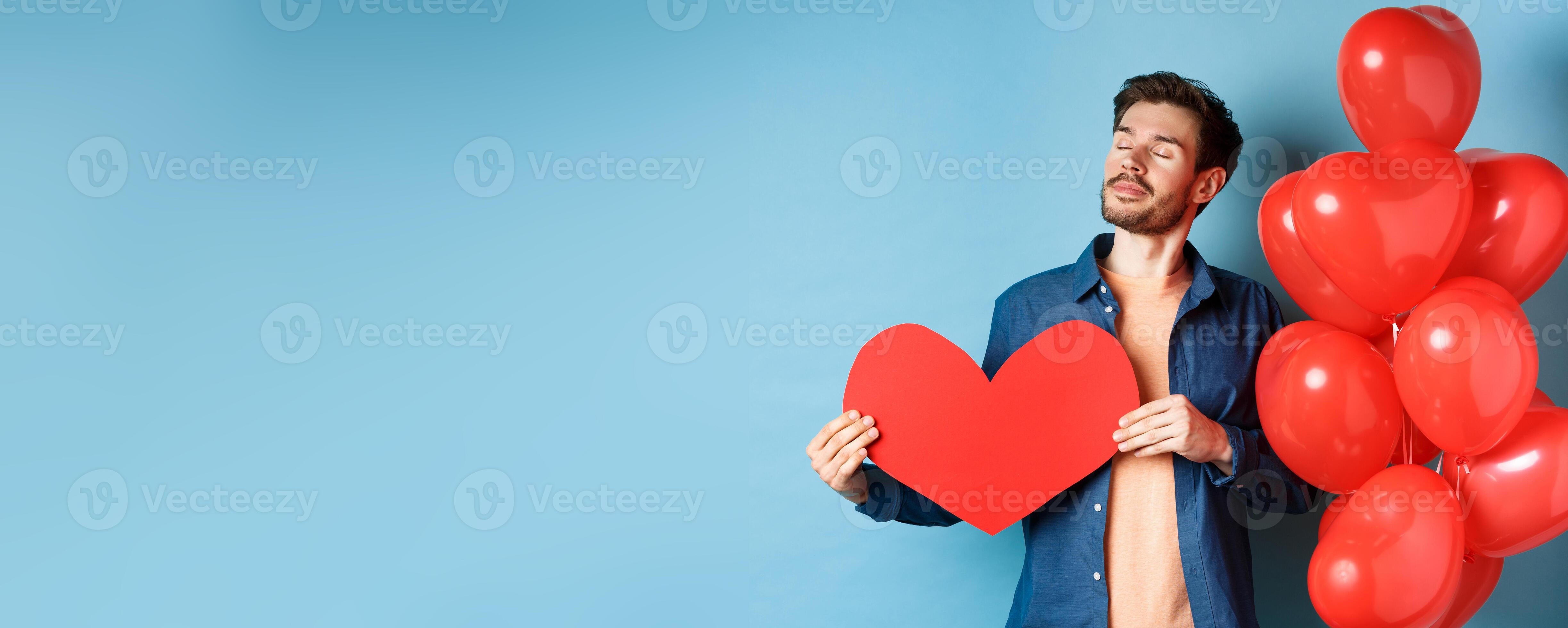 Valentines day and love concept. Dreamy man with closed eyes, holding romantic red heart cutout ...