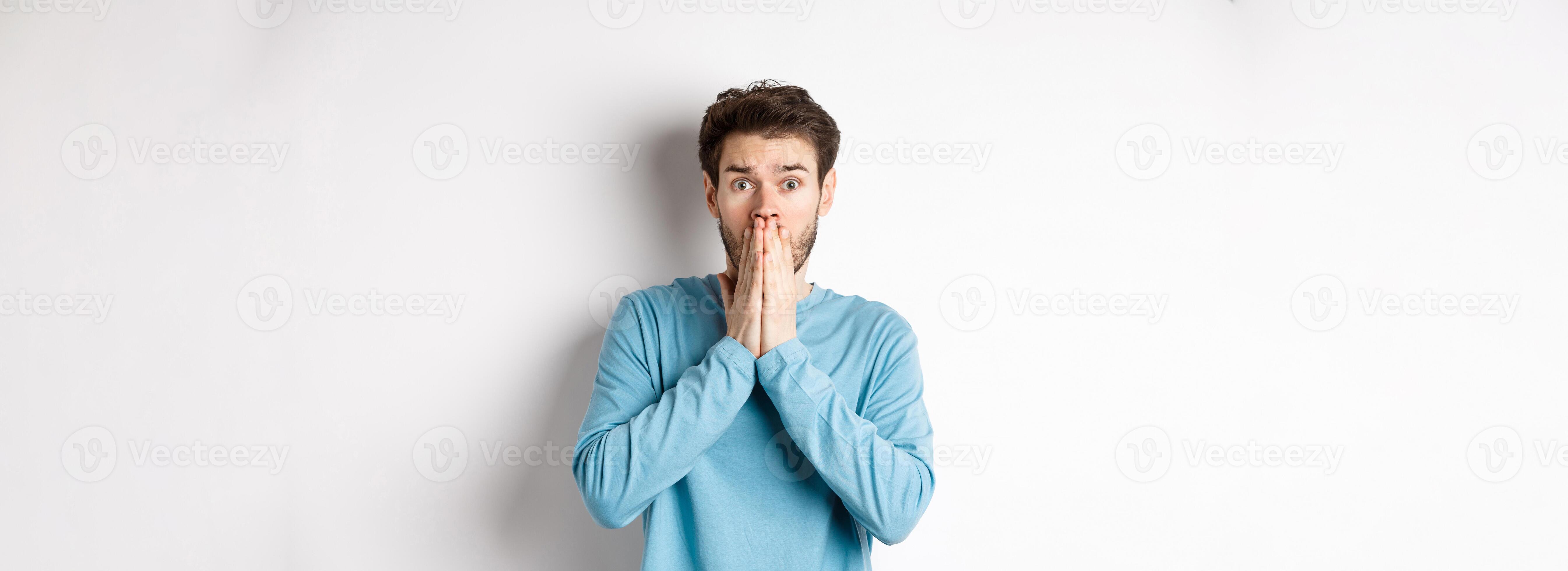 Shocked and worried young man gasping and covering mouth, look with ...