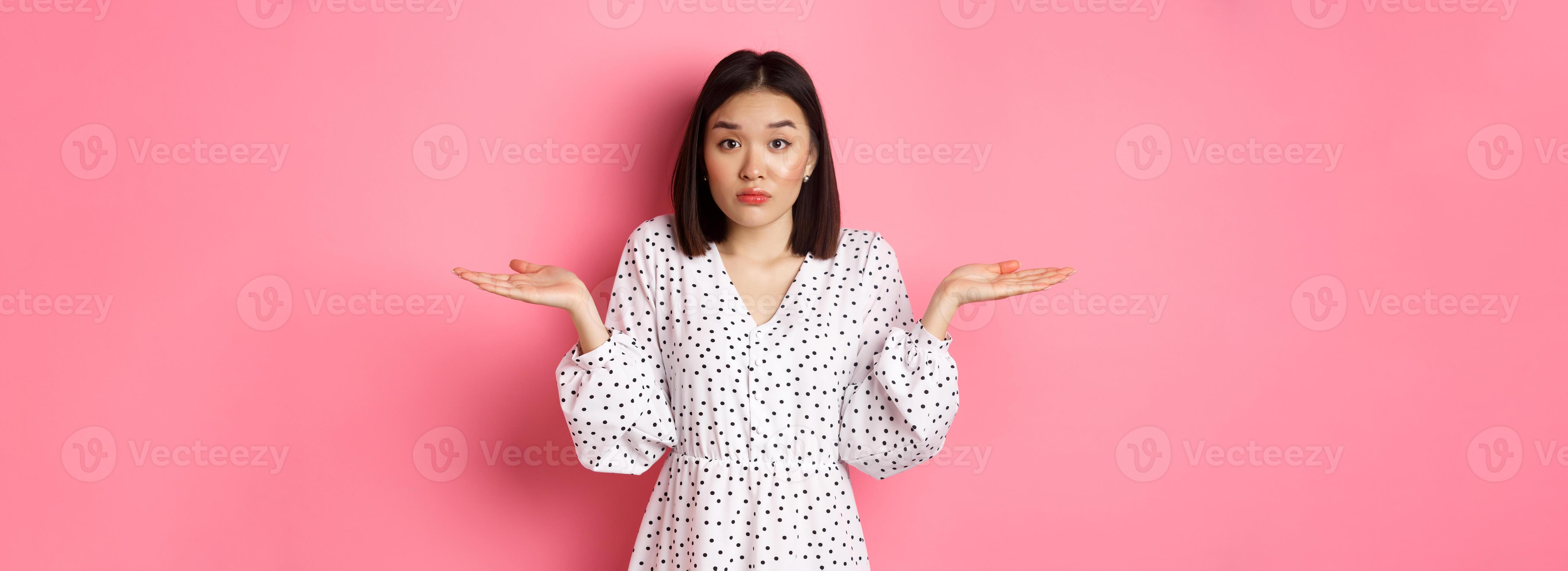 Indecisive cute asian woman shrugging, holding hands spread sideways on ...