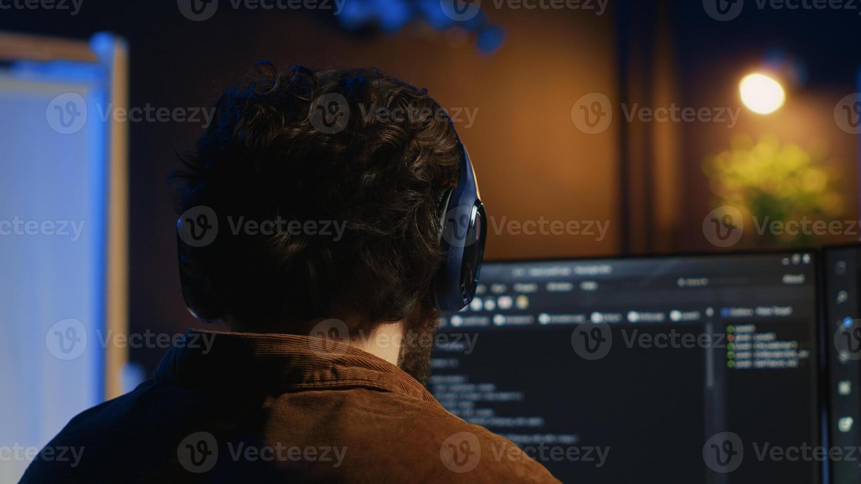 Technician putting headphones on while using coding to fortify firewalls, teleworking for IT ...