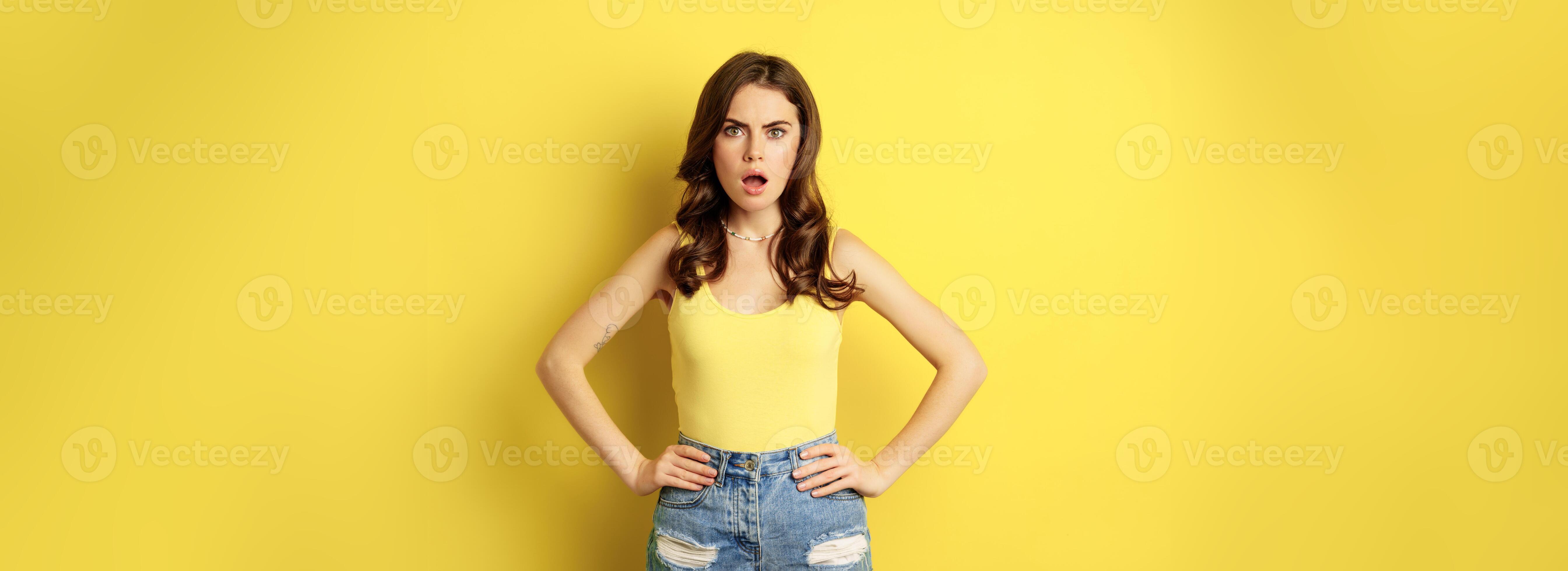 Shocked stylish girl hold hands on waist, drop jaw and stare confused at camera, posing in ...