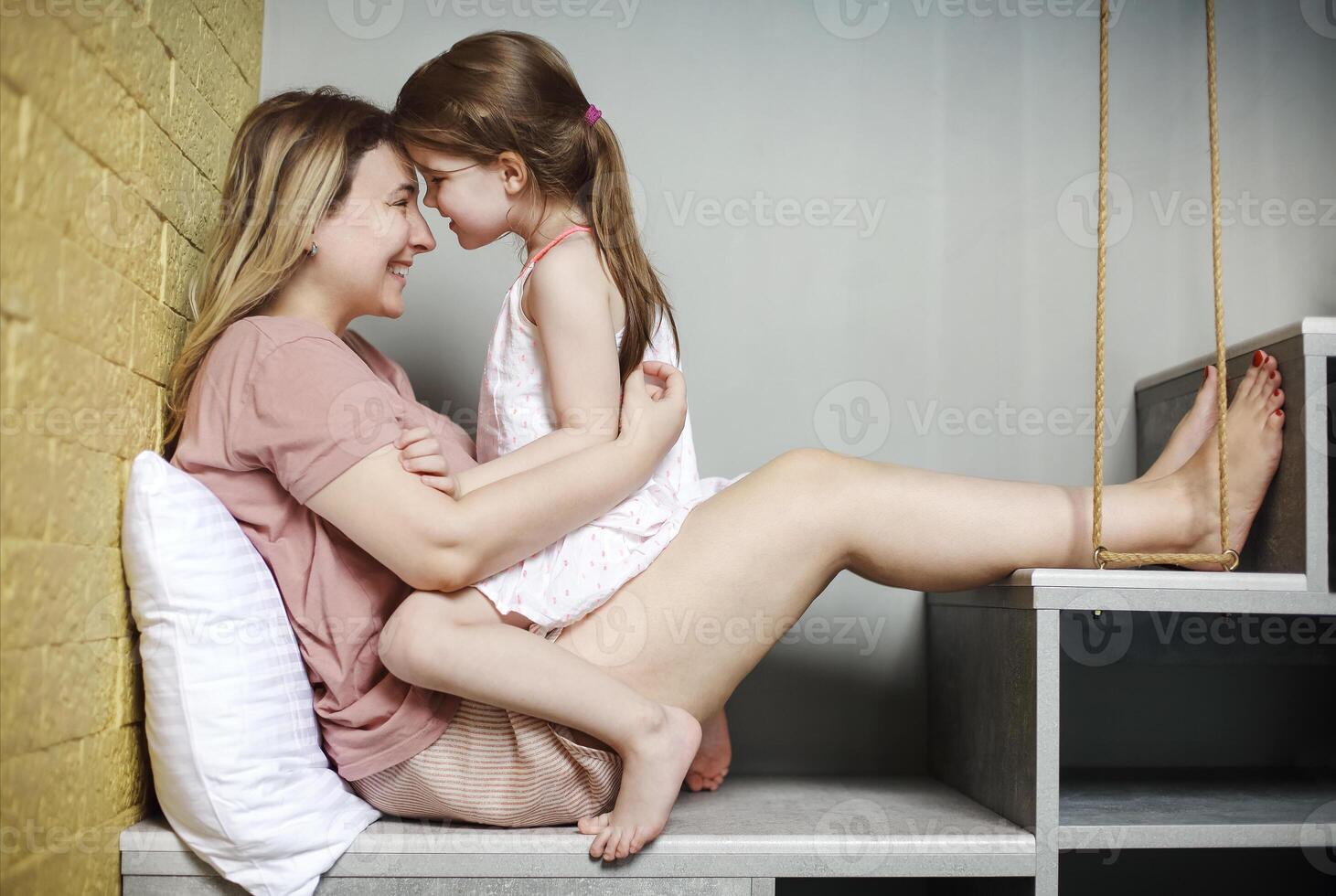 Young loving mother hugging embracing with her cute little daughter while sitting together on ...