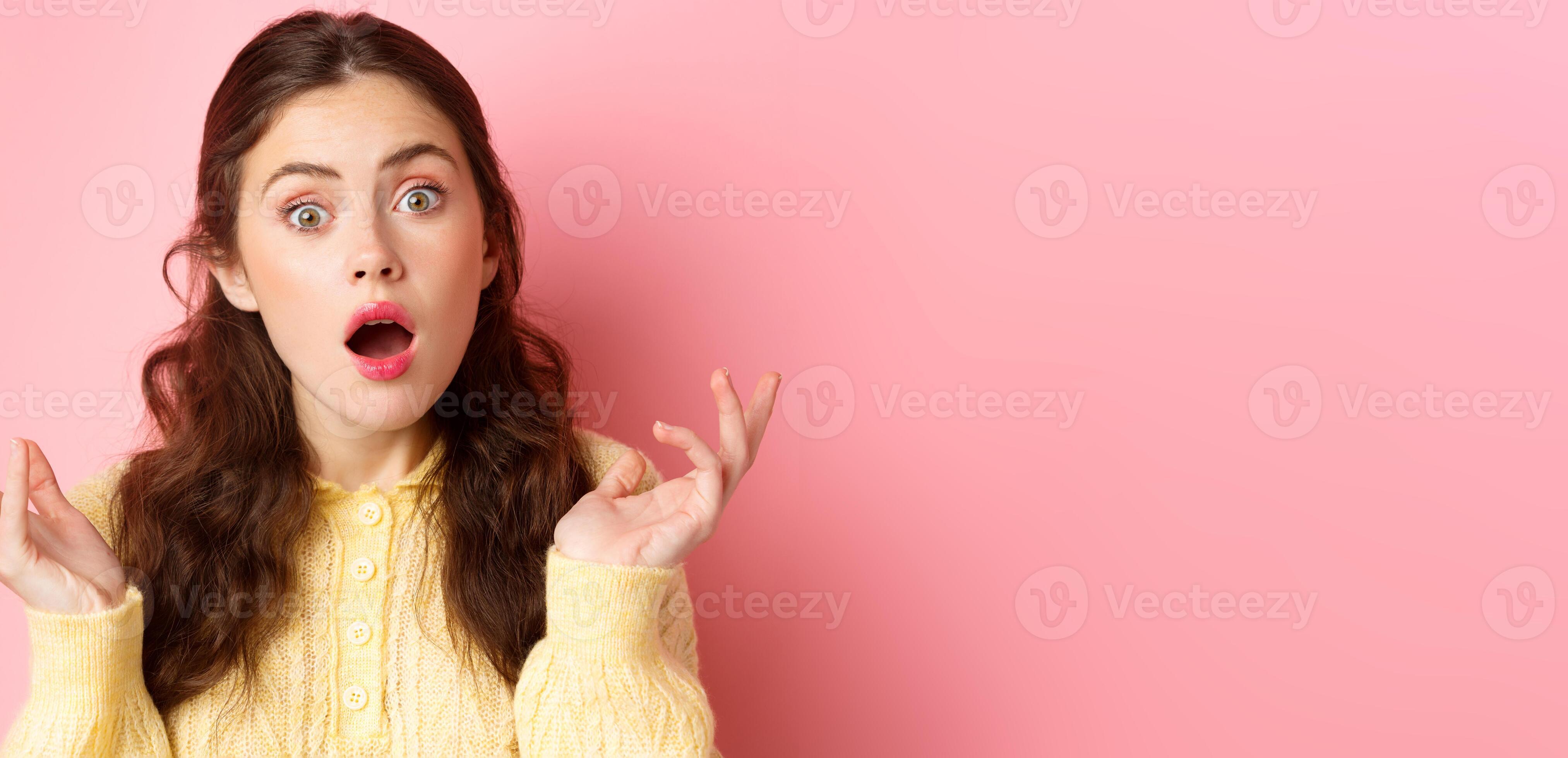 Close up of surprised and confused young woman open mouth and raise hands, stare at camera ...