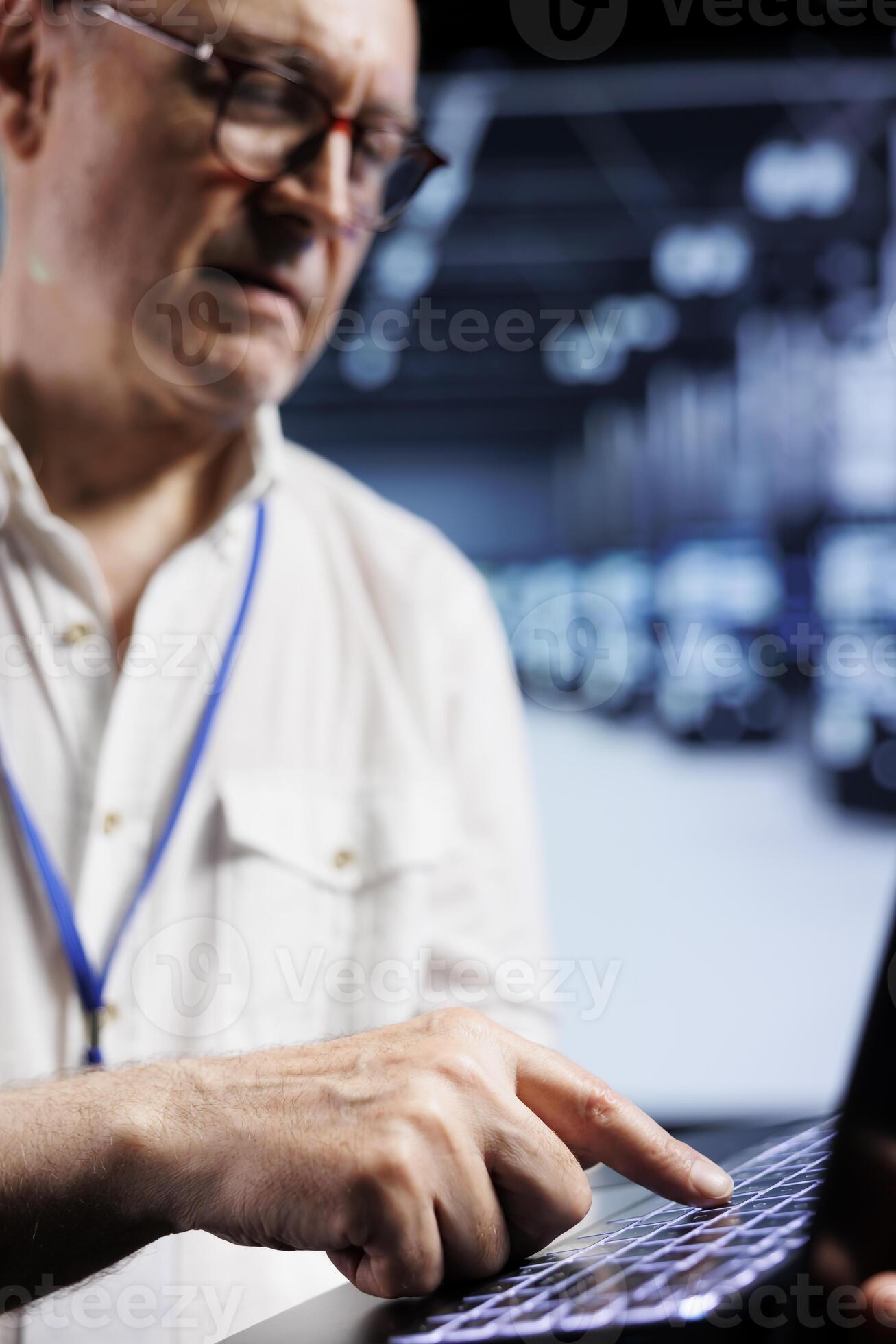 Aged IT programmer using laptop to examine server clusters for power fluctuations. Seasoned ...