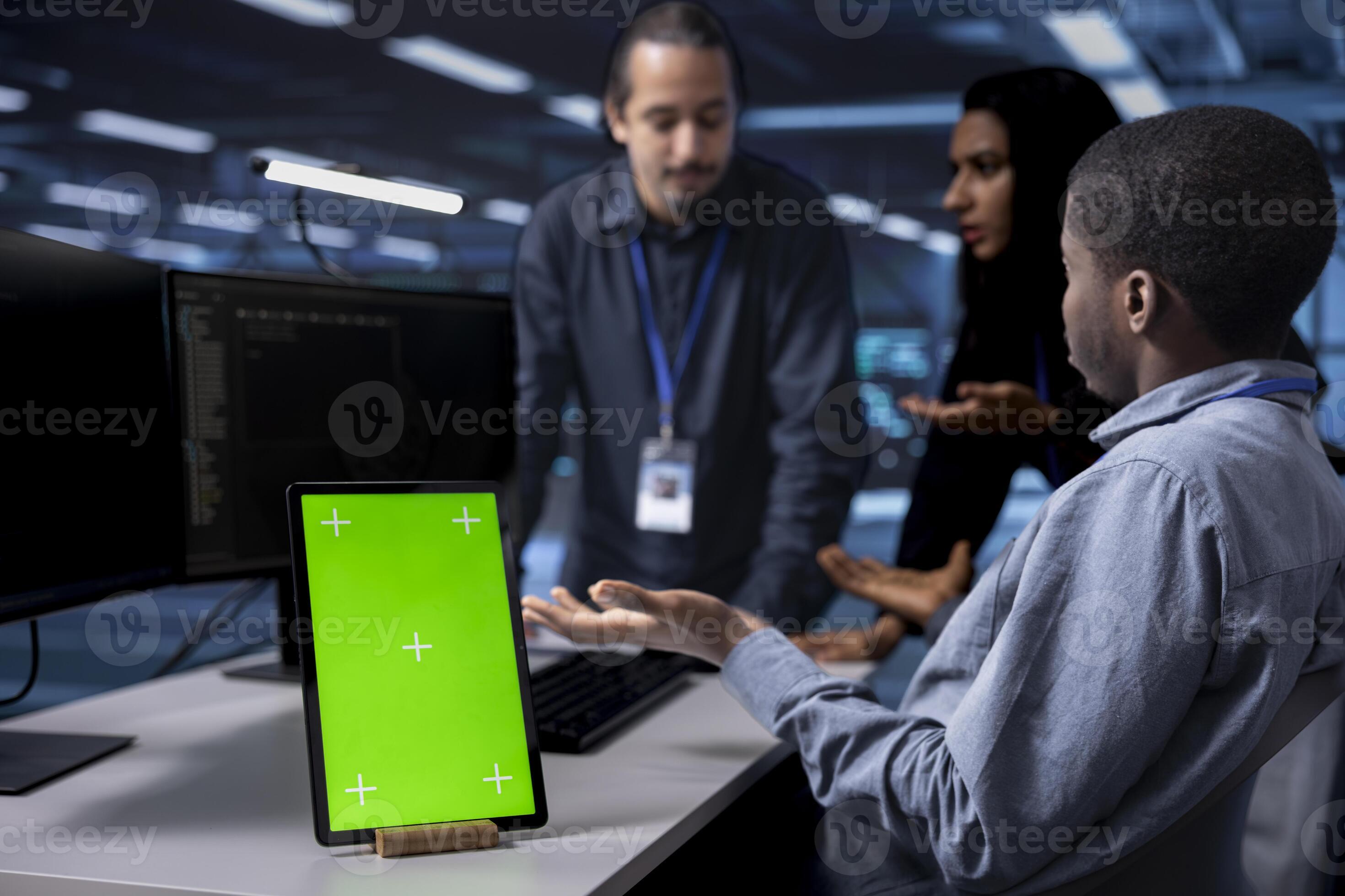 Focus on green screen tablet used by team in blurry background reconfiguring server farm to ...