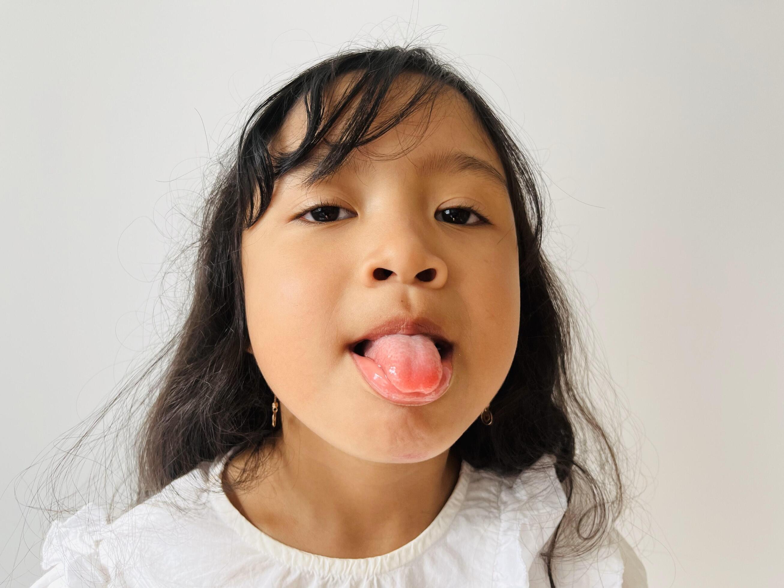 Five year old Asian child wearing a white shirt with a mocking gesture by sticking out her ...