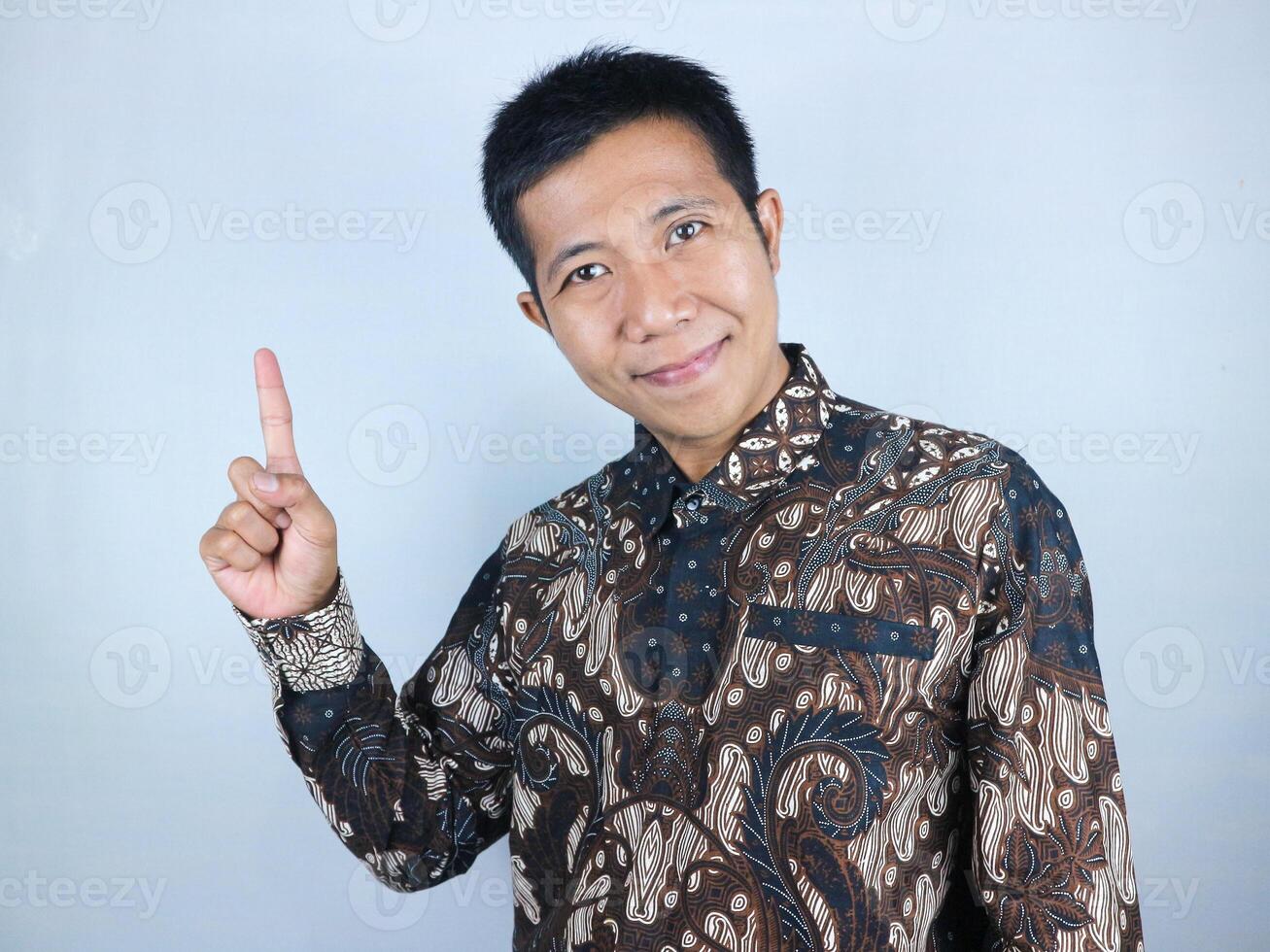 Smiling expression of asian man wearing batik clothes pointing up ...