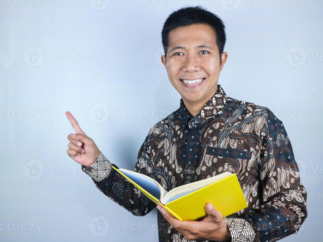 Adult Asian man wearing batik clothes smiling and pointing beside while ...